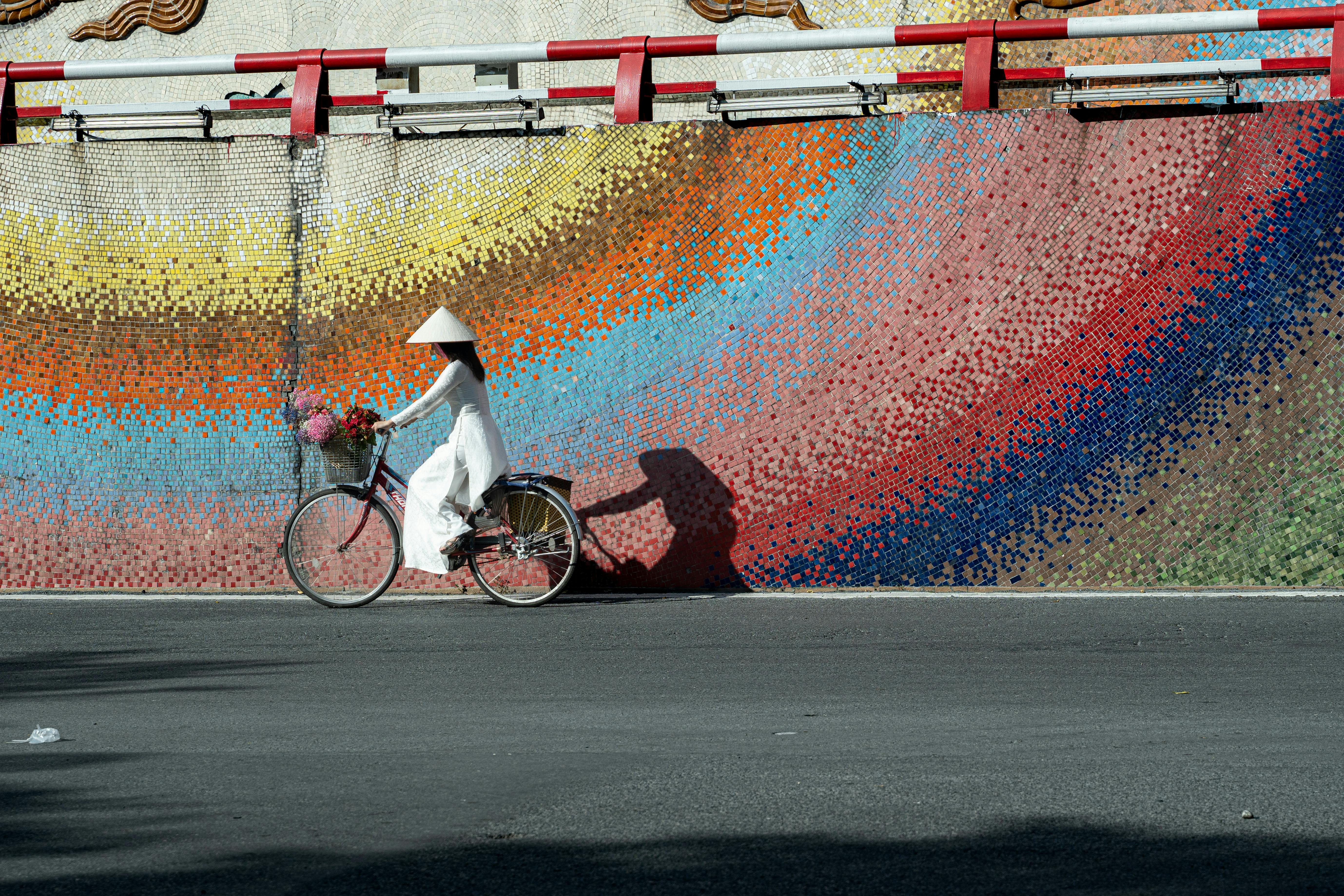 Vietnamese Woman Cycling Past Ceramic Mosaic Wall · Free Stock Photo