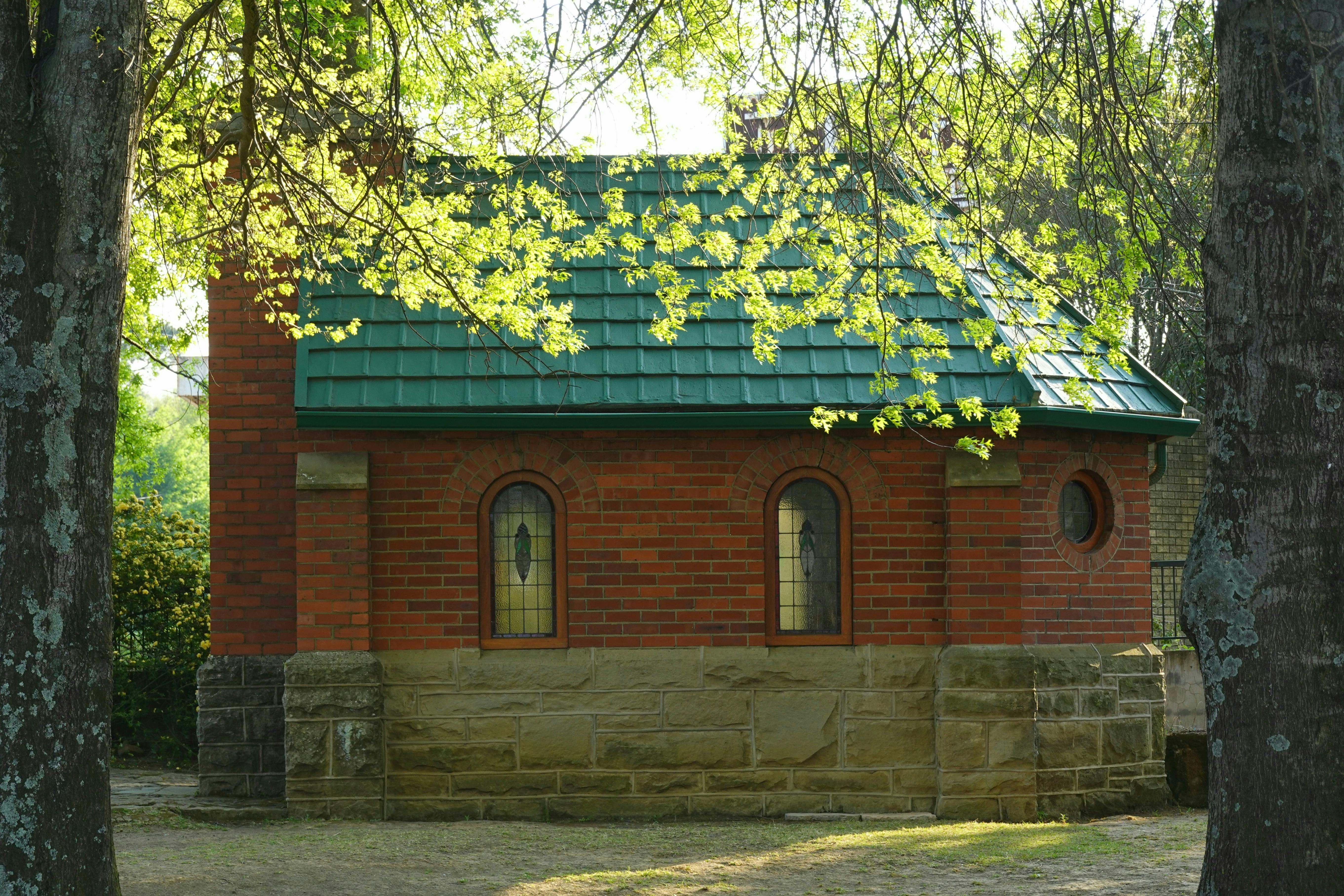 Quaint Brick Chapel with Green Roof Surrounded by Trees · Free Stock Photo