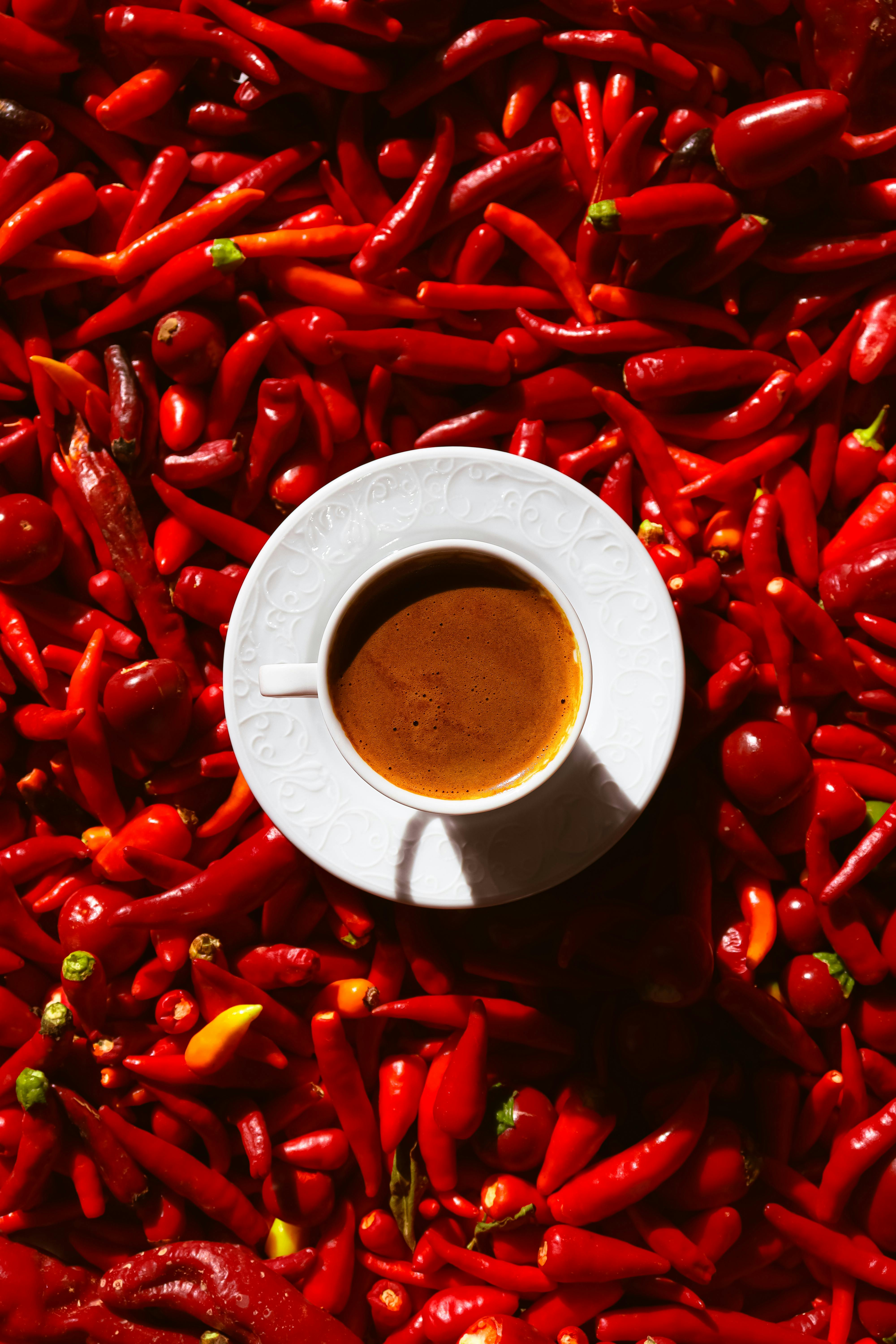 Coffee in White Cup Surrounded by Red Chili Peppers · Free Stock Photo