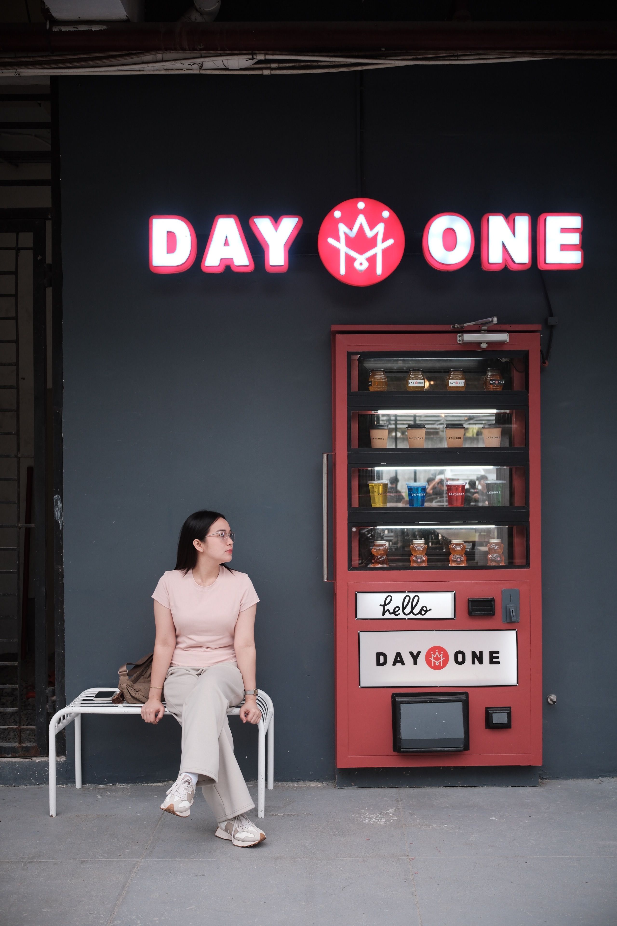 Woman Sitting by Vending Machine with 'DAY ONE' Sign · Free Stock Photo