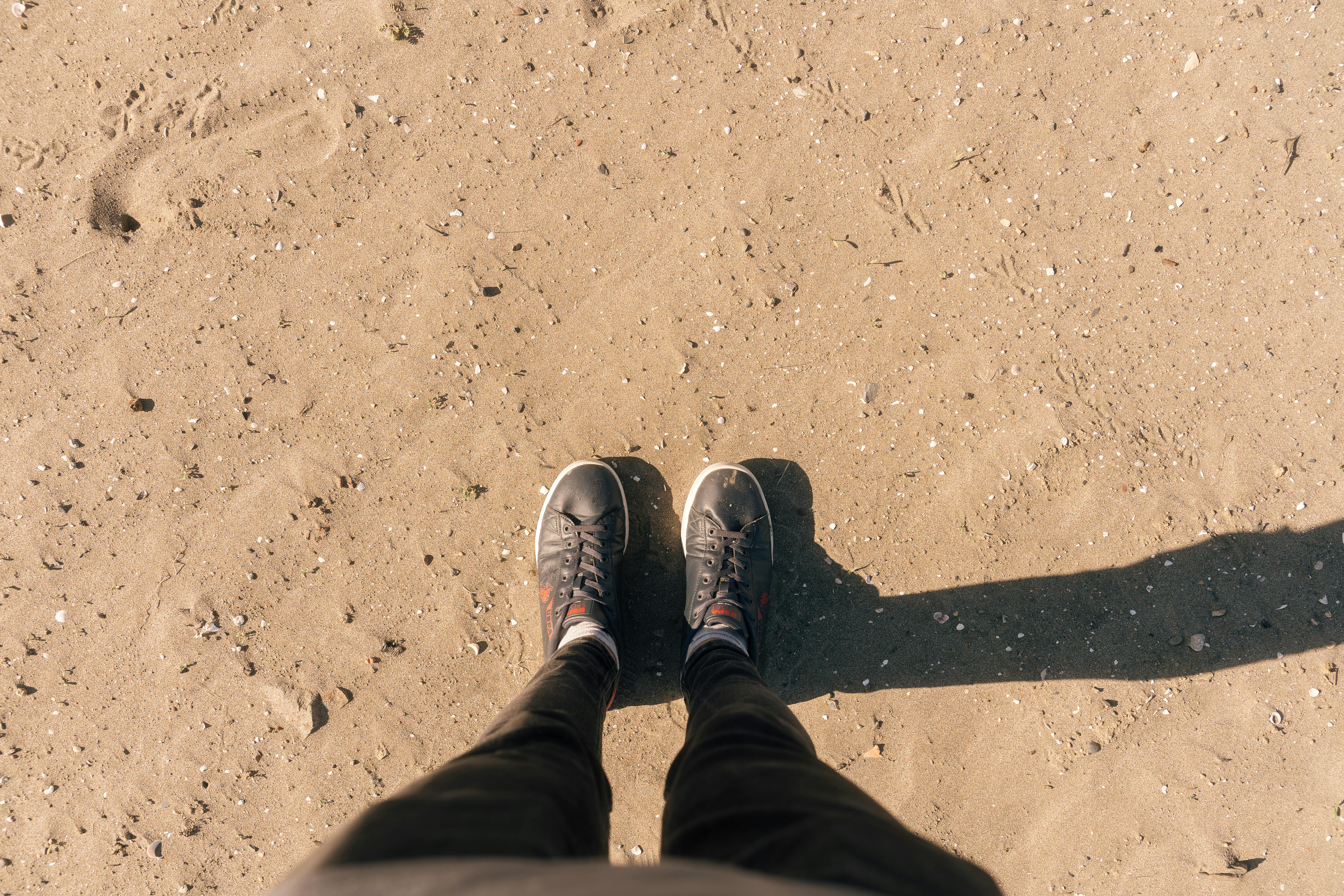 Casual Shoes on Sandy Beach Foot Perspective · Free Stock Photo