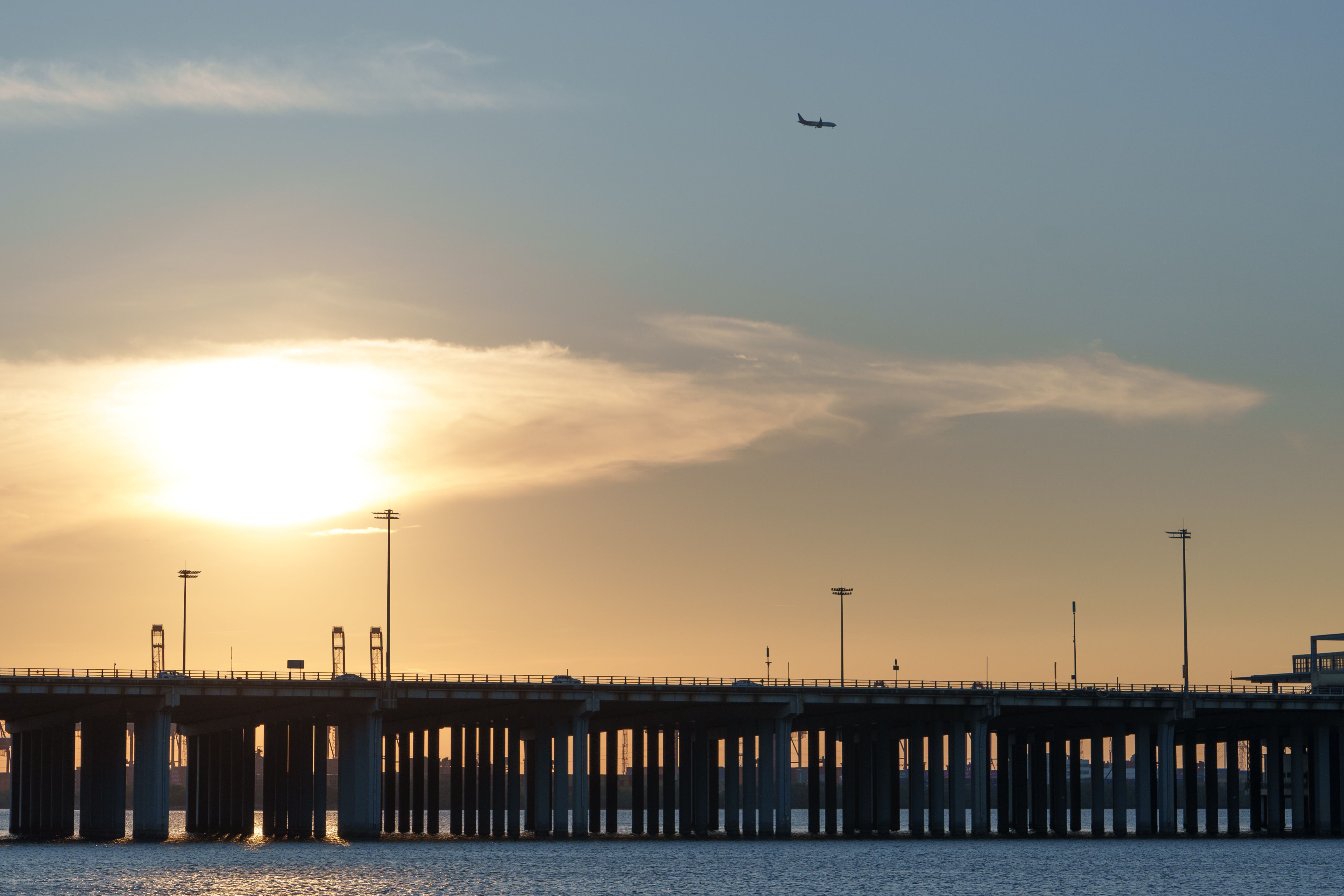 Sunset Over Bridge with Airplane in Sky · Free Stock Photo