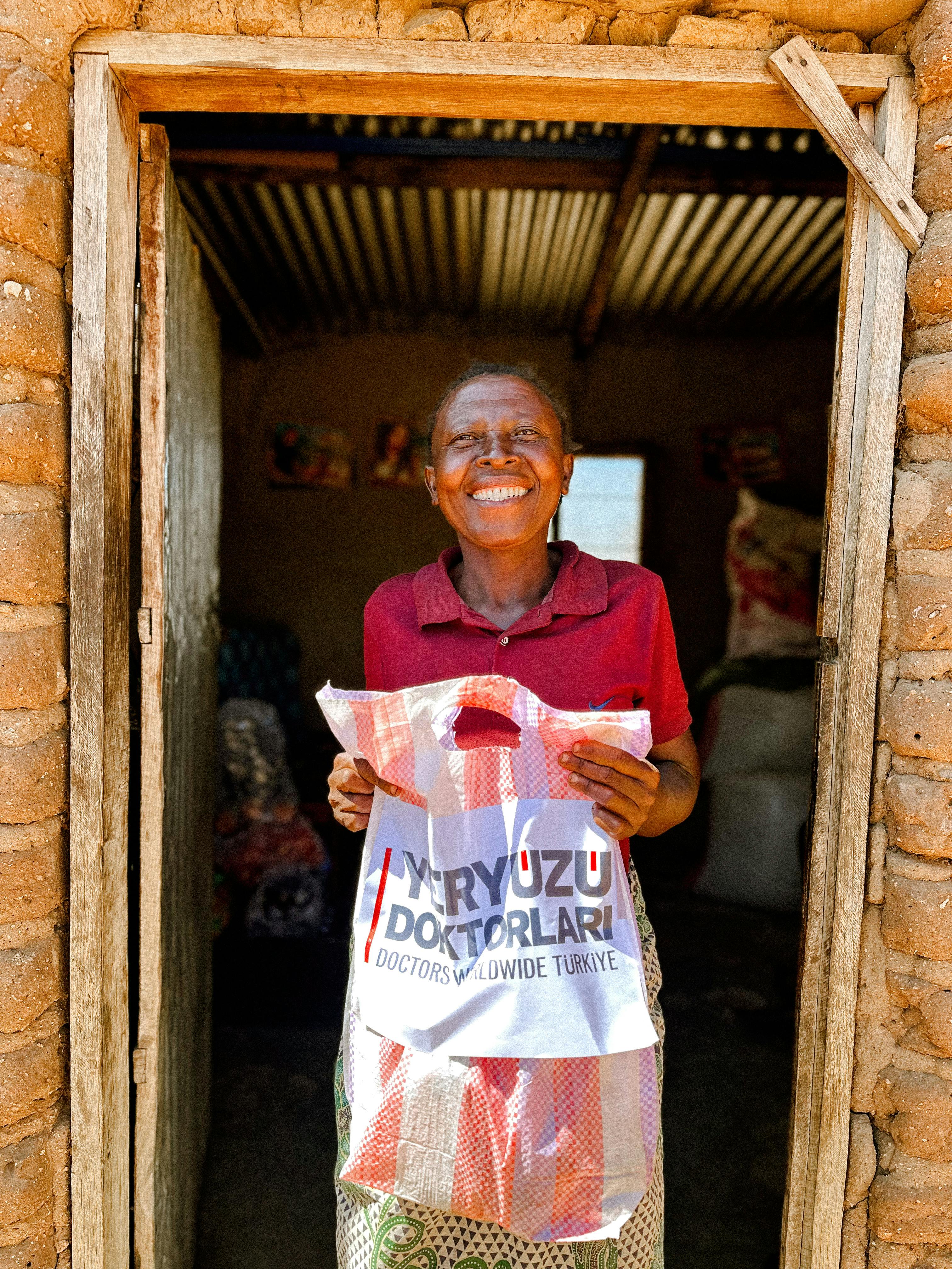 Happy Woman Holding Donation Bag in Rural Doorway · Free Stock Photo
