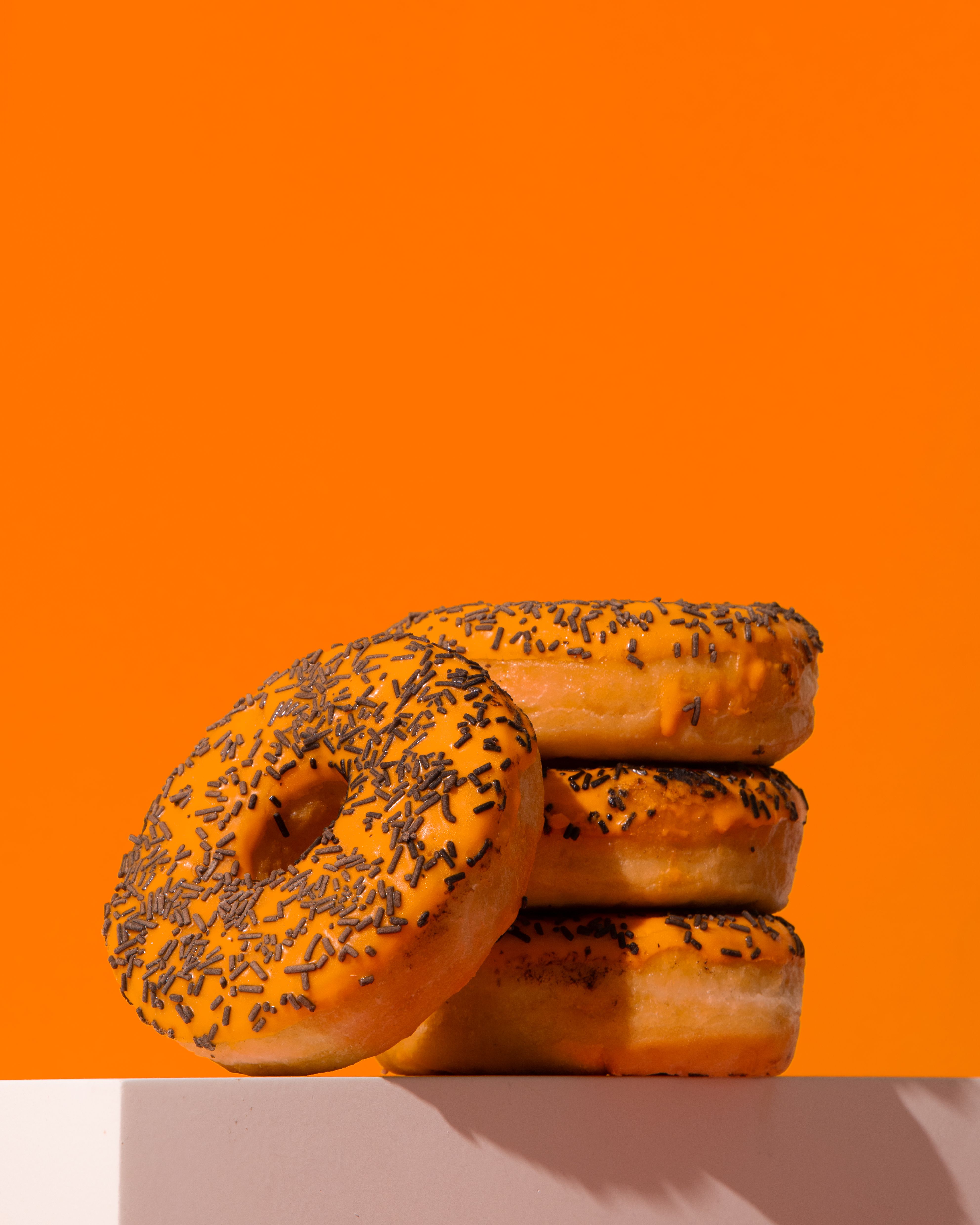Stack of Orange Iced Donuts with Sprinkles · Free Stock Photo