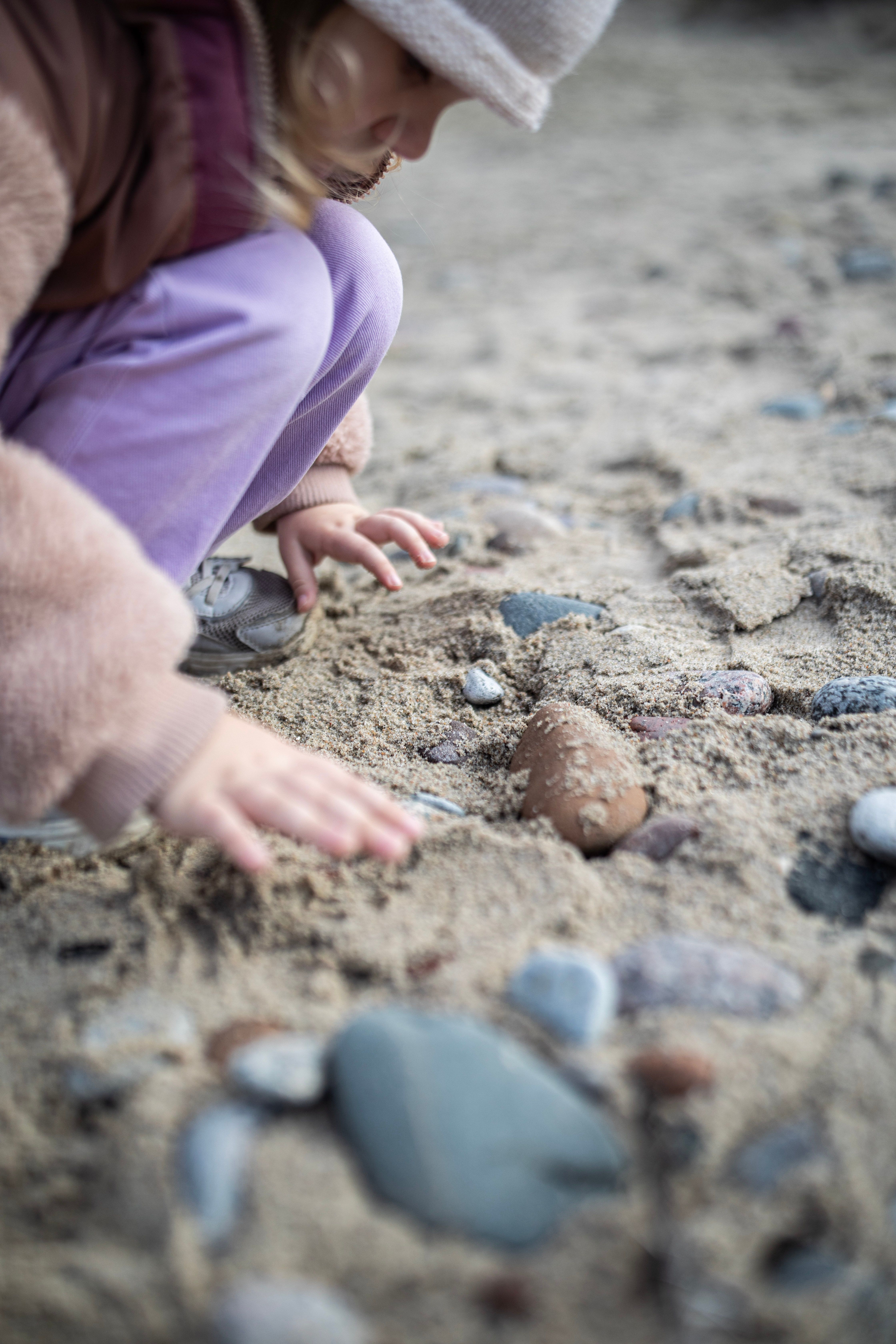 Child Playing with Stones on Sandy Beach · Free Stock Photo