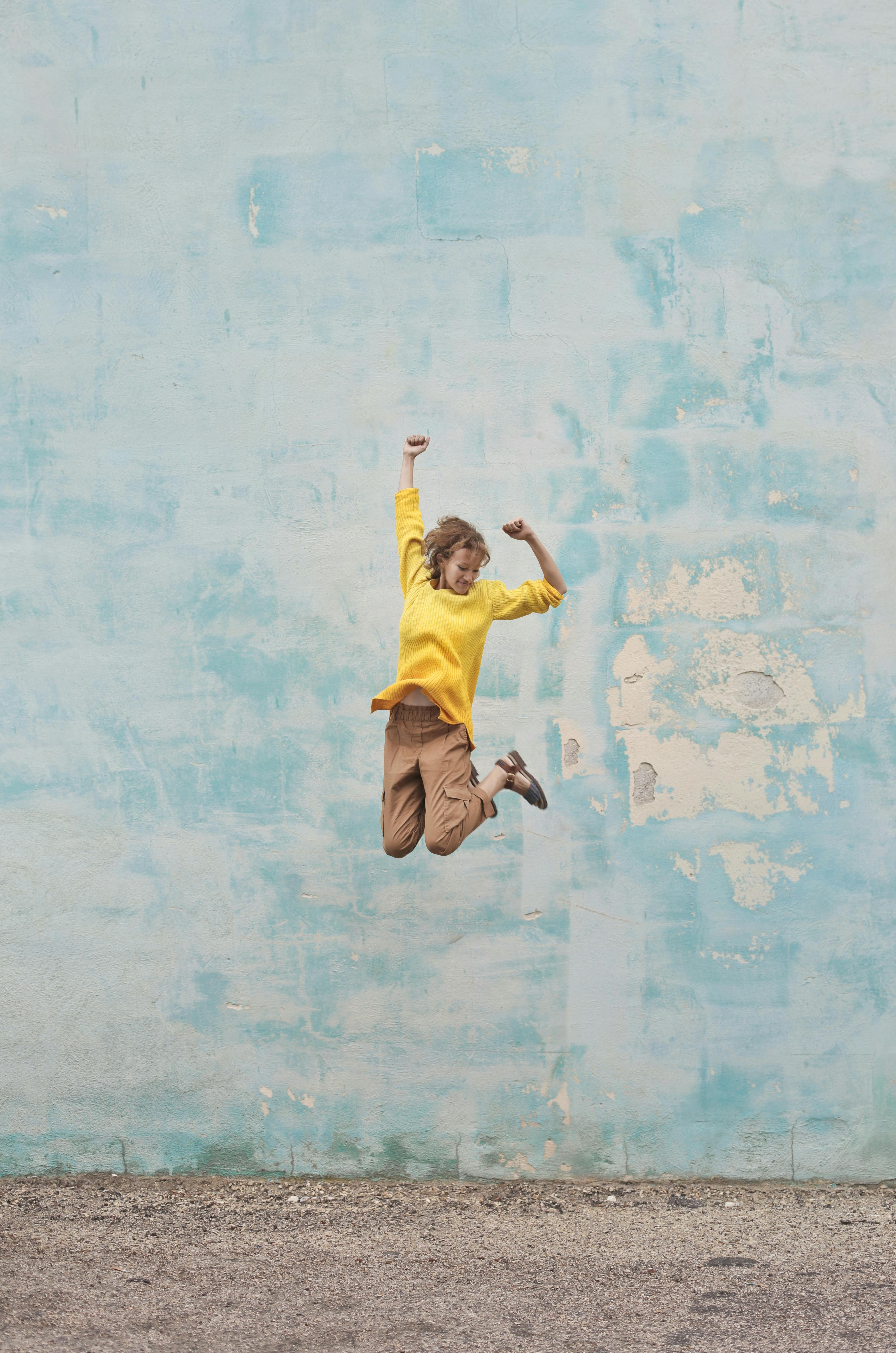 Joyful Child Leaping Against Rustic Blue Wall · Free Stock Photo
