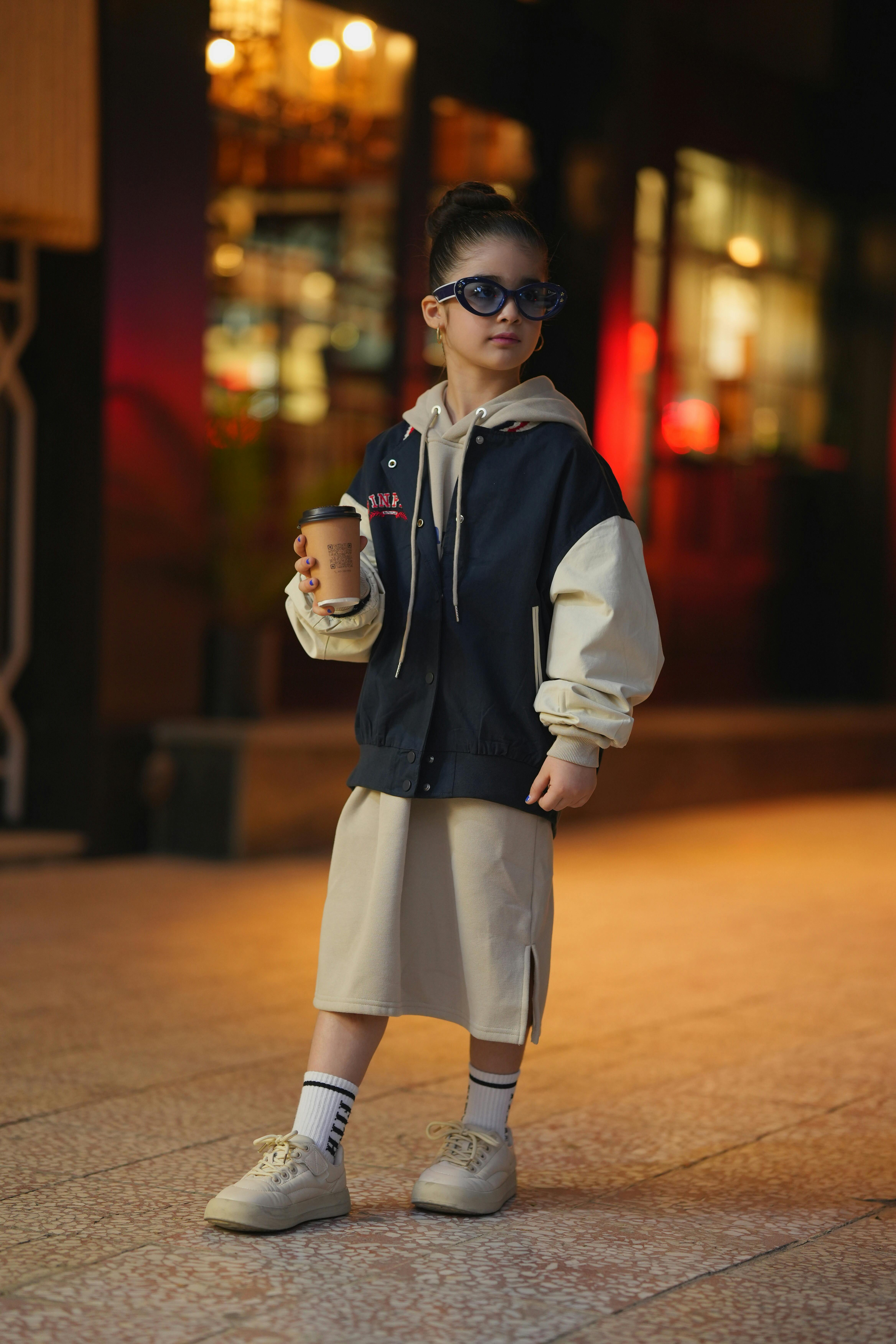 Stylish Child Poses with Beverage on Urban Street · Free Stock Photo