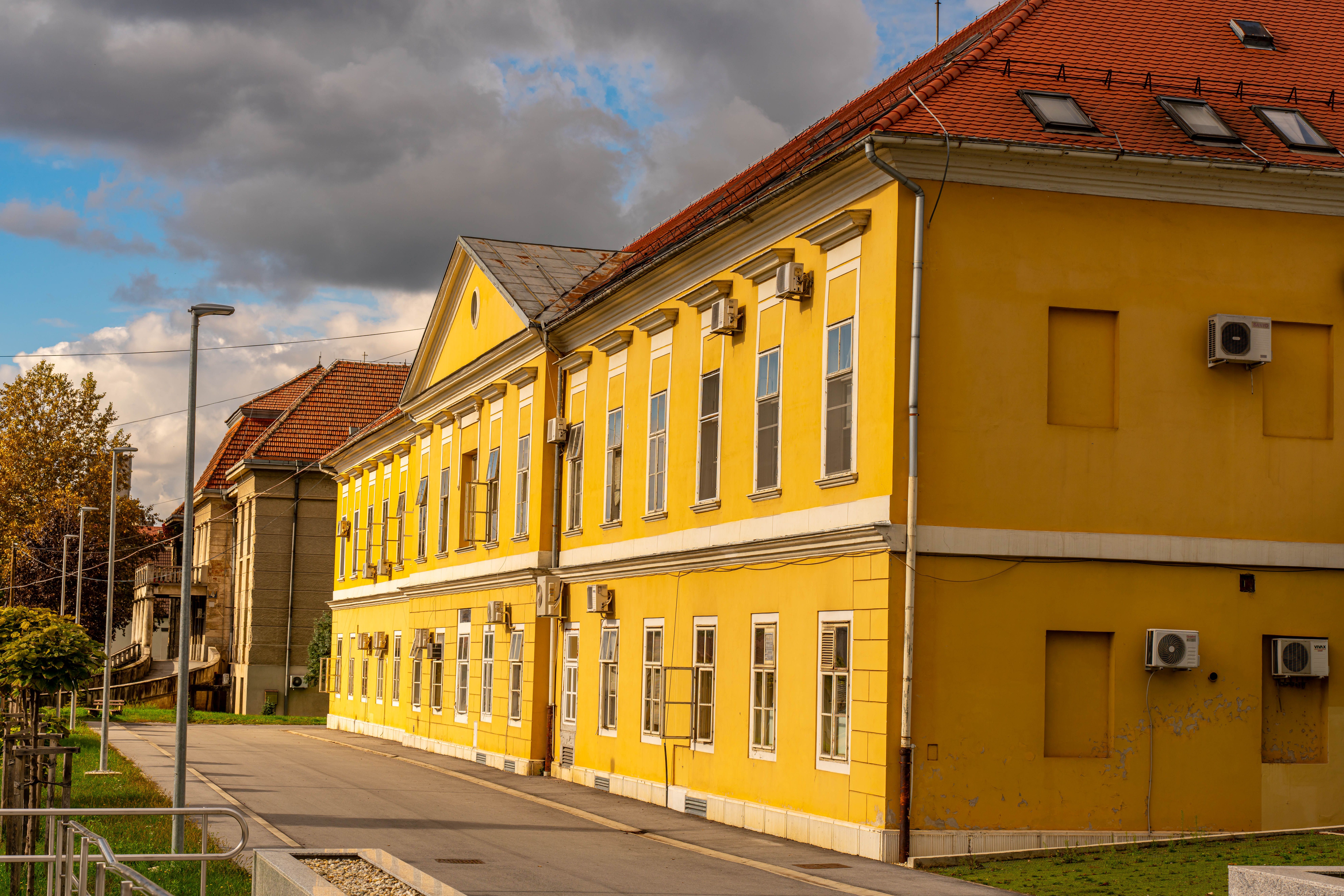 Historic Yellow Building with Red Roof on Cloudy Day · Free Stock Photo
