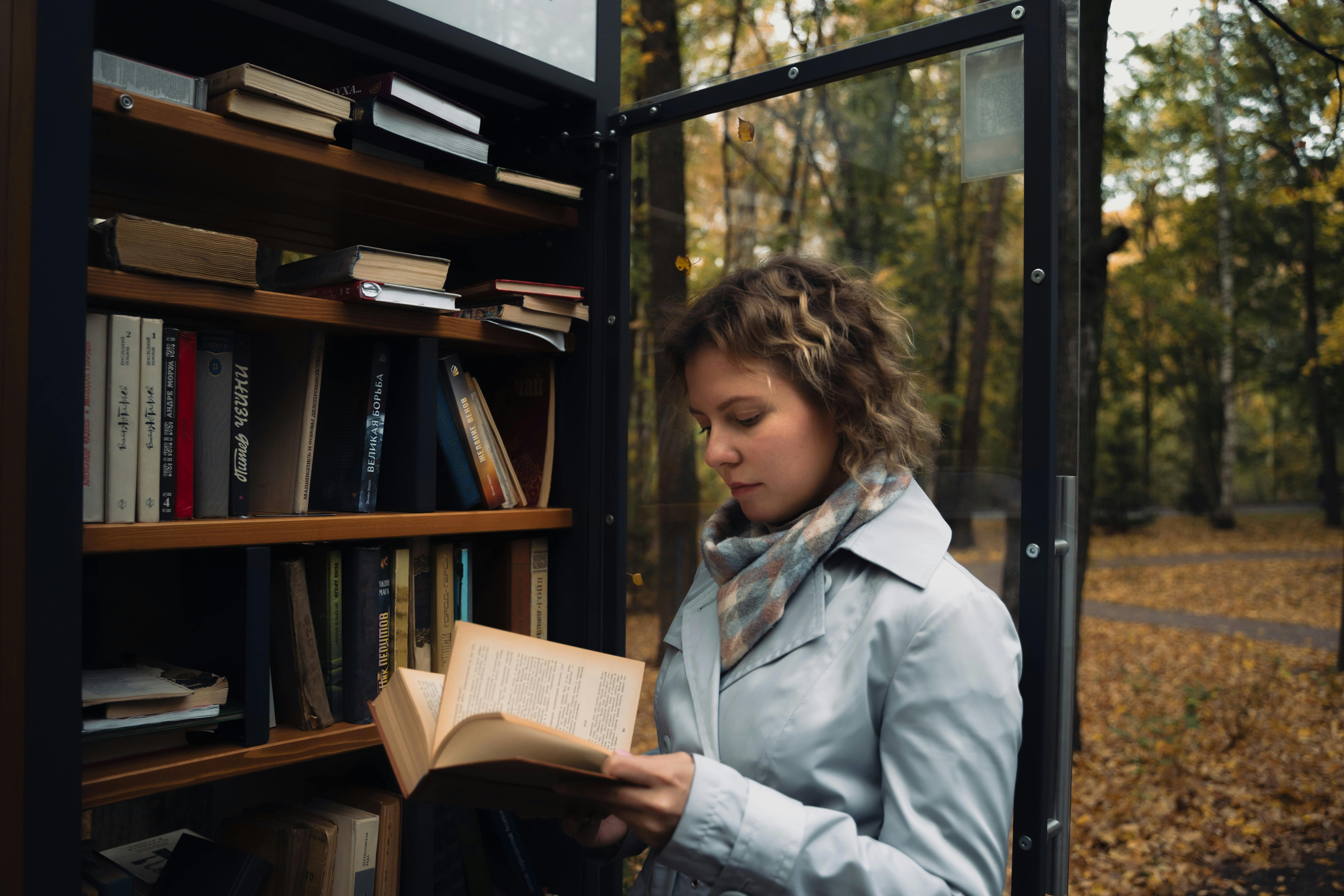 Young Woman Reading by Outdoor Bookcase in Autumn · Free Stock Photo