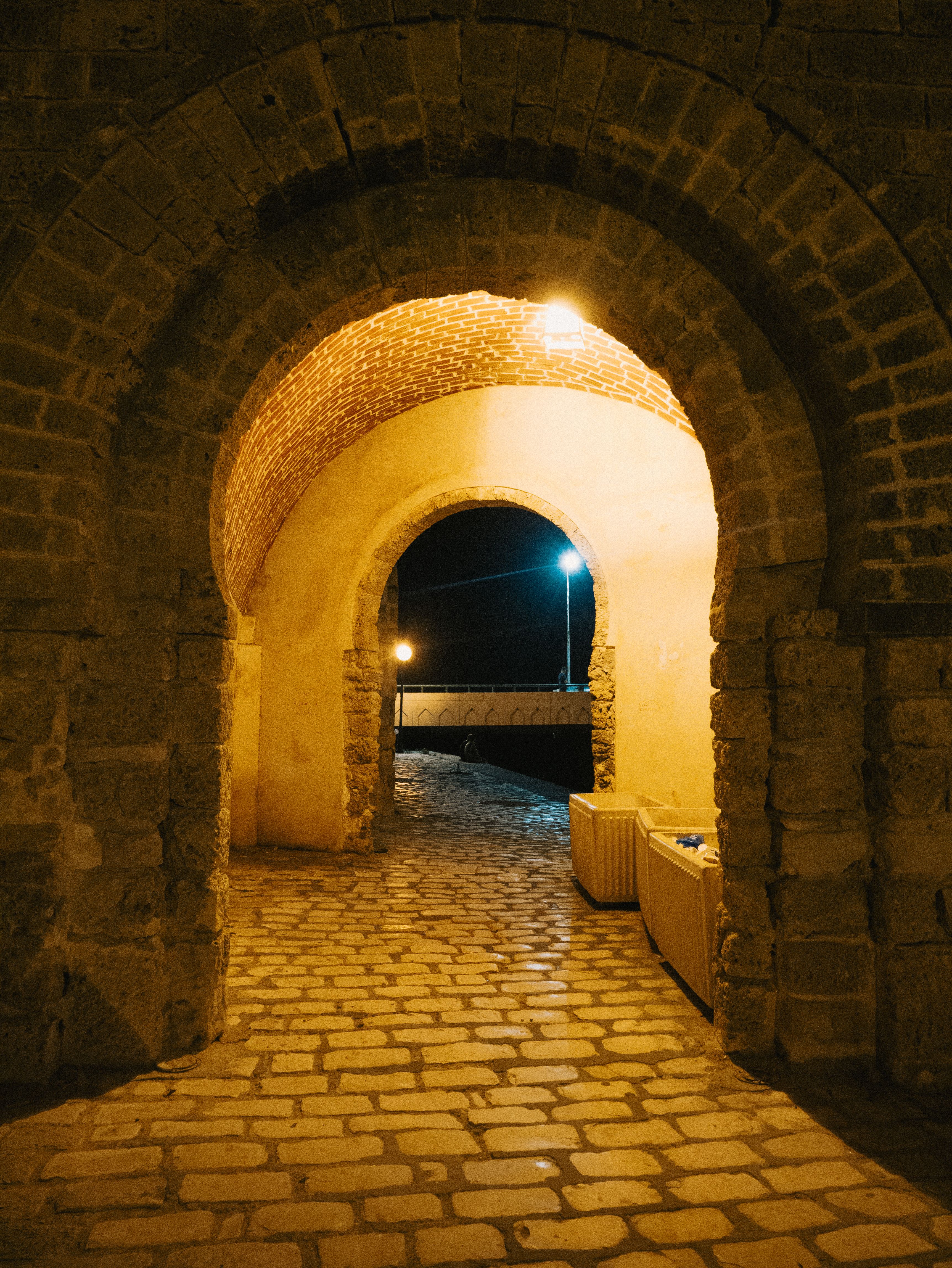 Arched stone corridor at night with warm lighting · Free Stock Photo