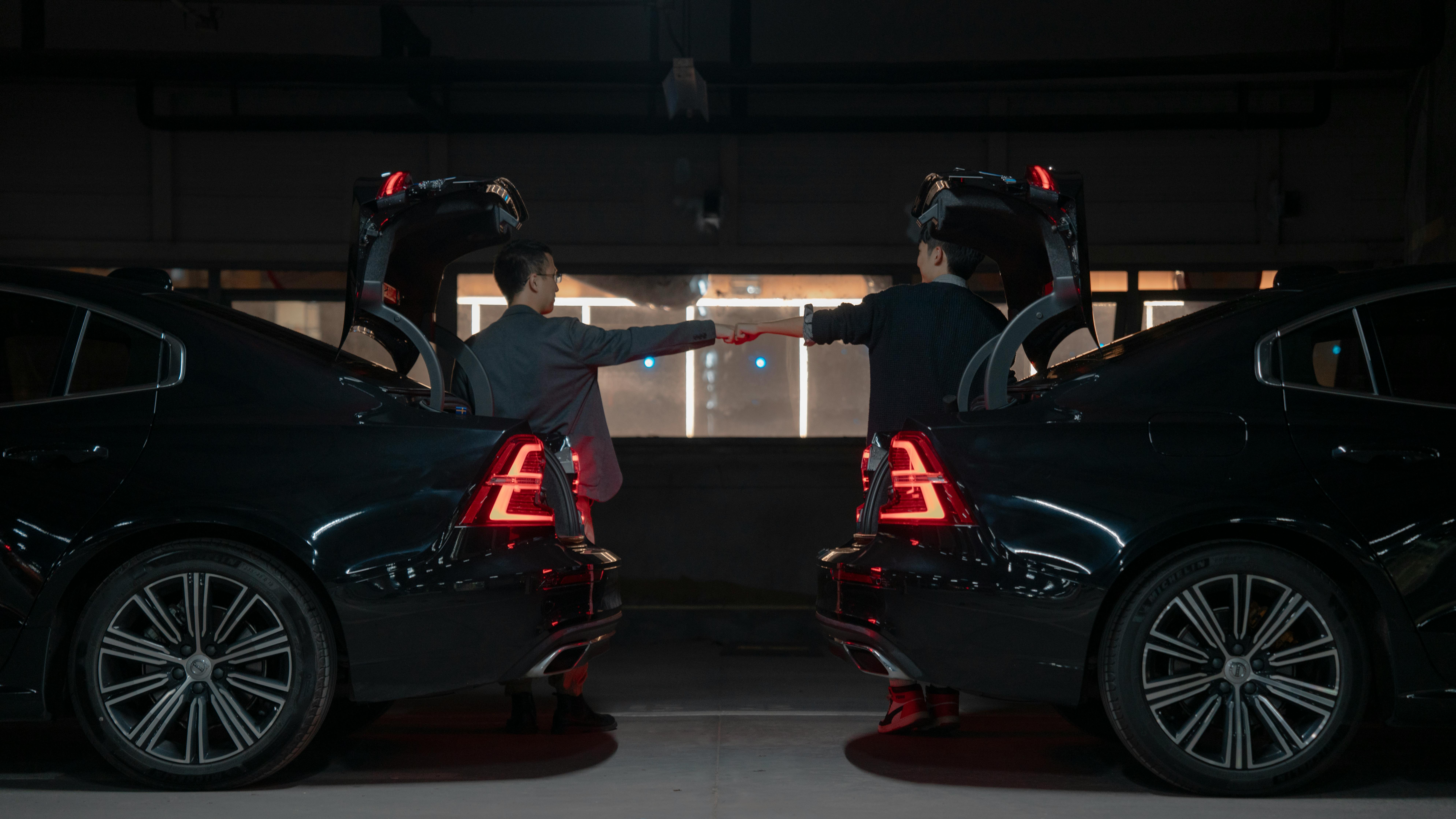 Two Men Fist Bumping Between Cars in Garage · Free Stock Photo