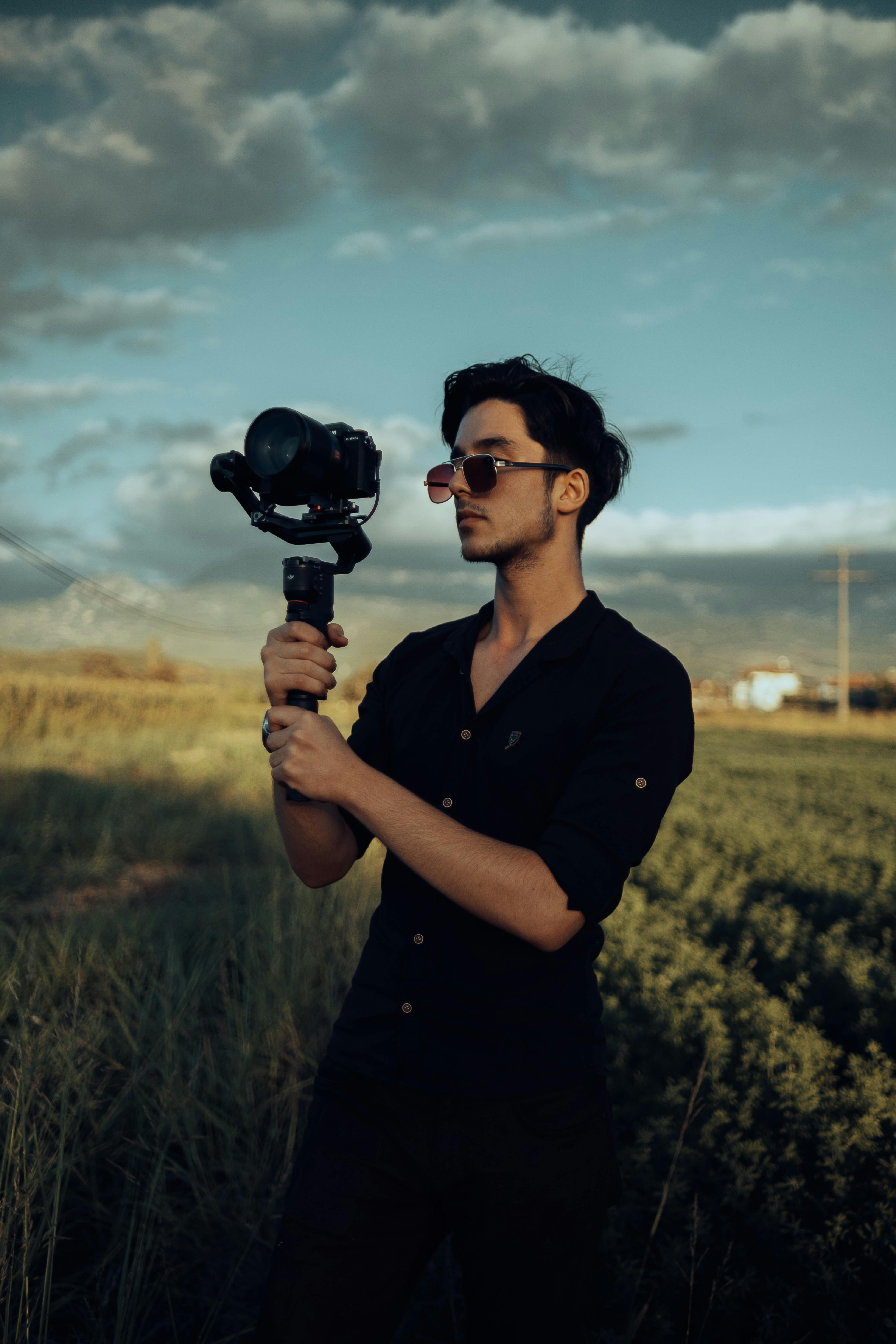 Young Filmmaker with Camera in Field at Dusk · Free Stock Photo