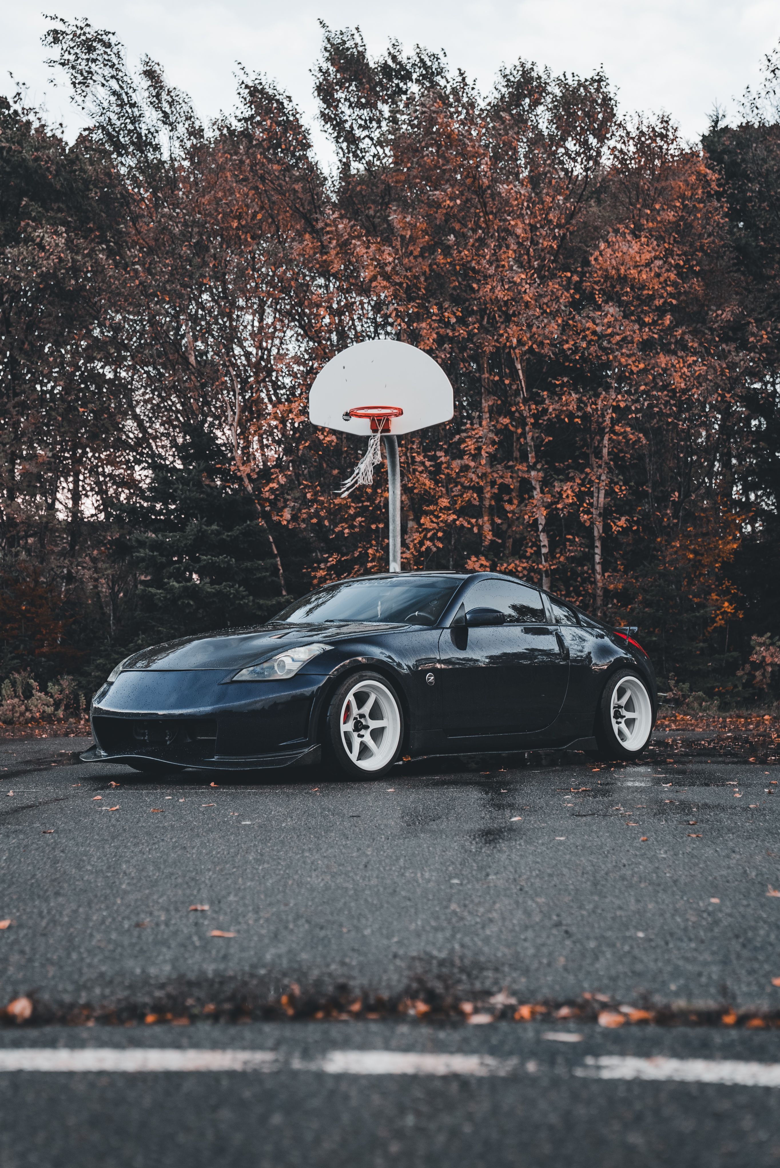 Sleek Black Sports Car on Autumn Basketball Court · Free Stock Photo