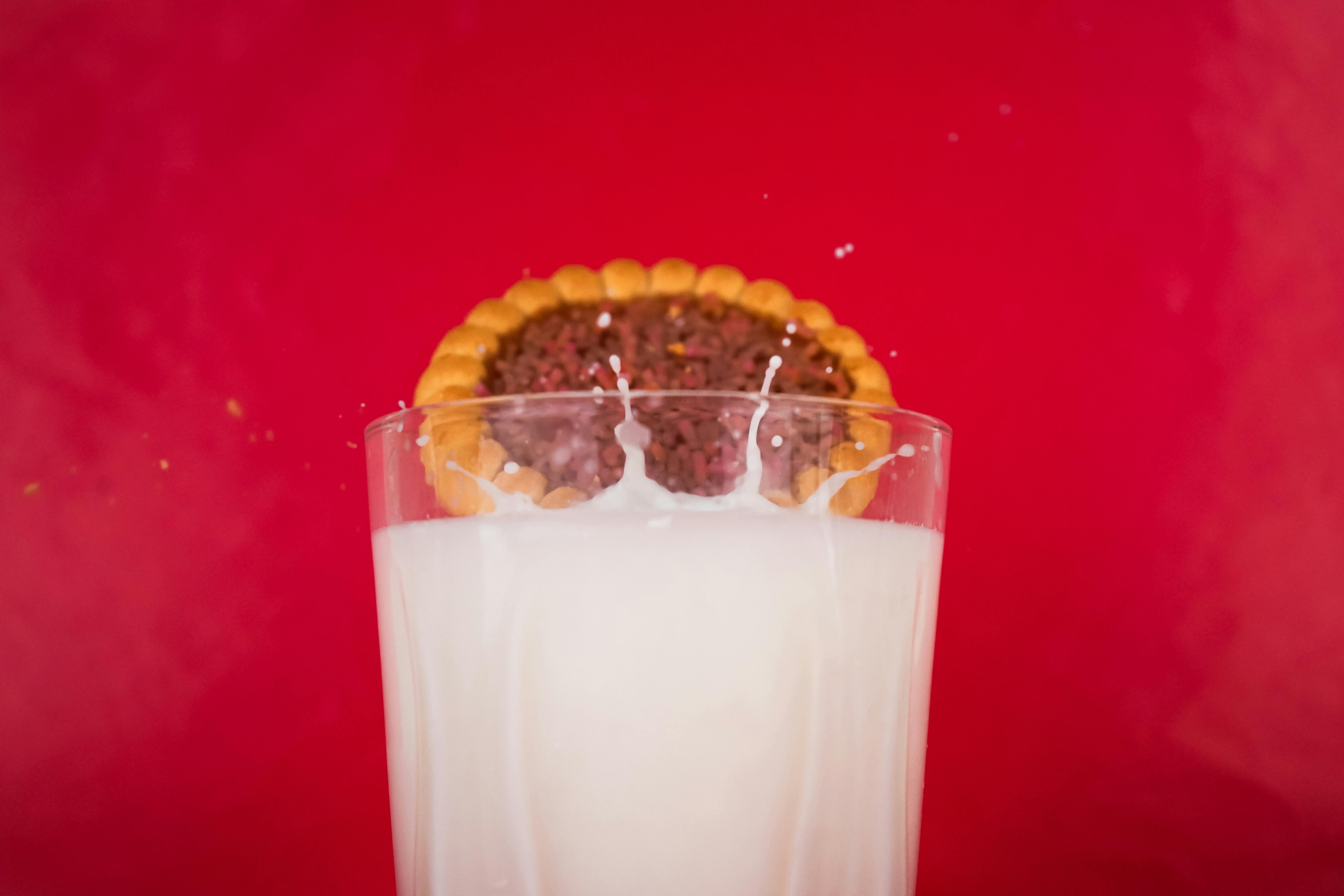 Cookie Splash in Milk with Vibrant Red Background · Free Stock Photo