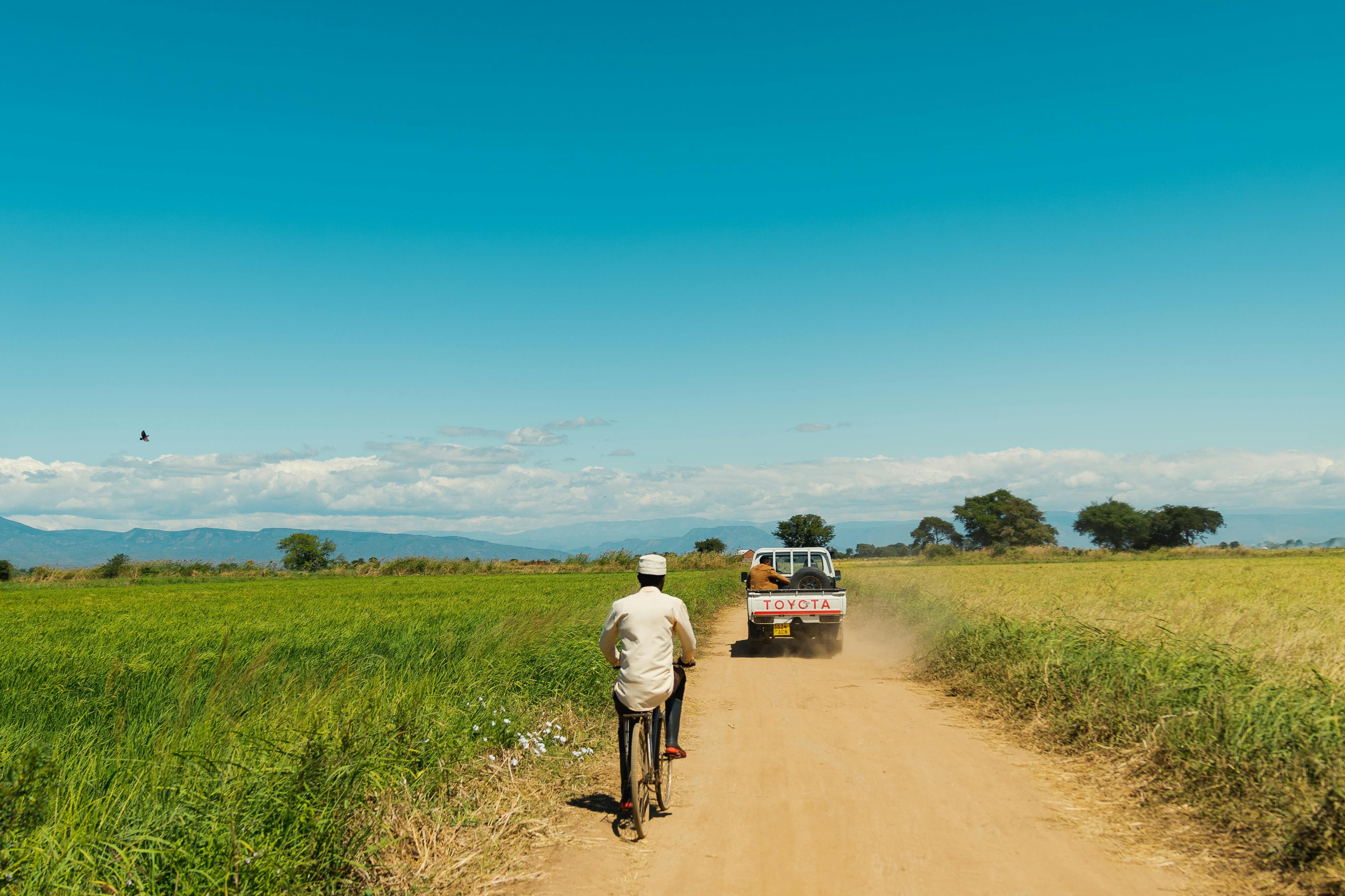 Rural African Landscape with Cyclist and Vehicle · Free Stock Photo