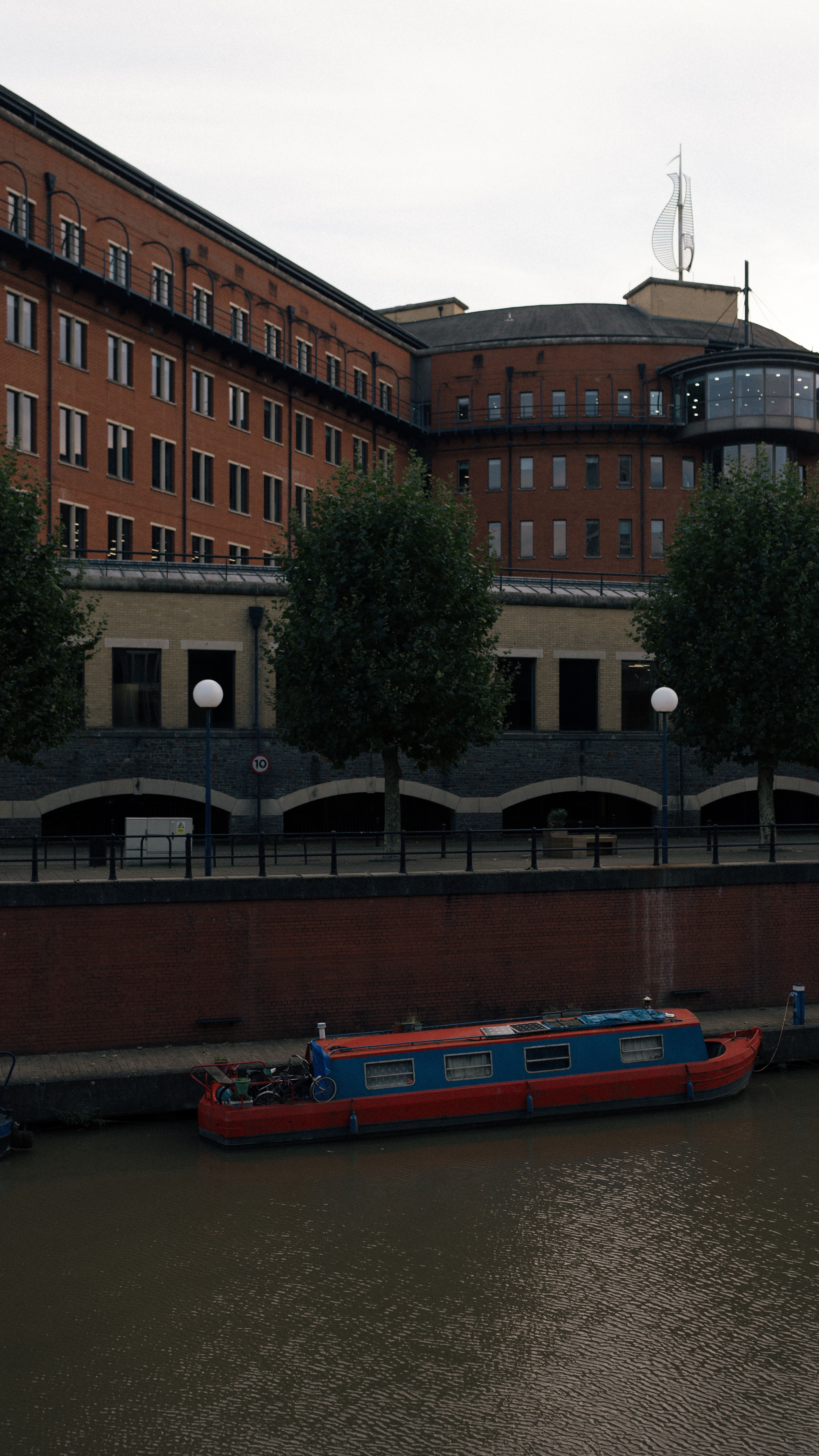 Bright canal boat by imposing brick building · Free Stock Photo
