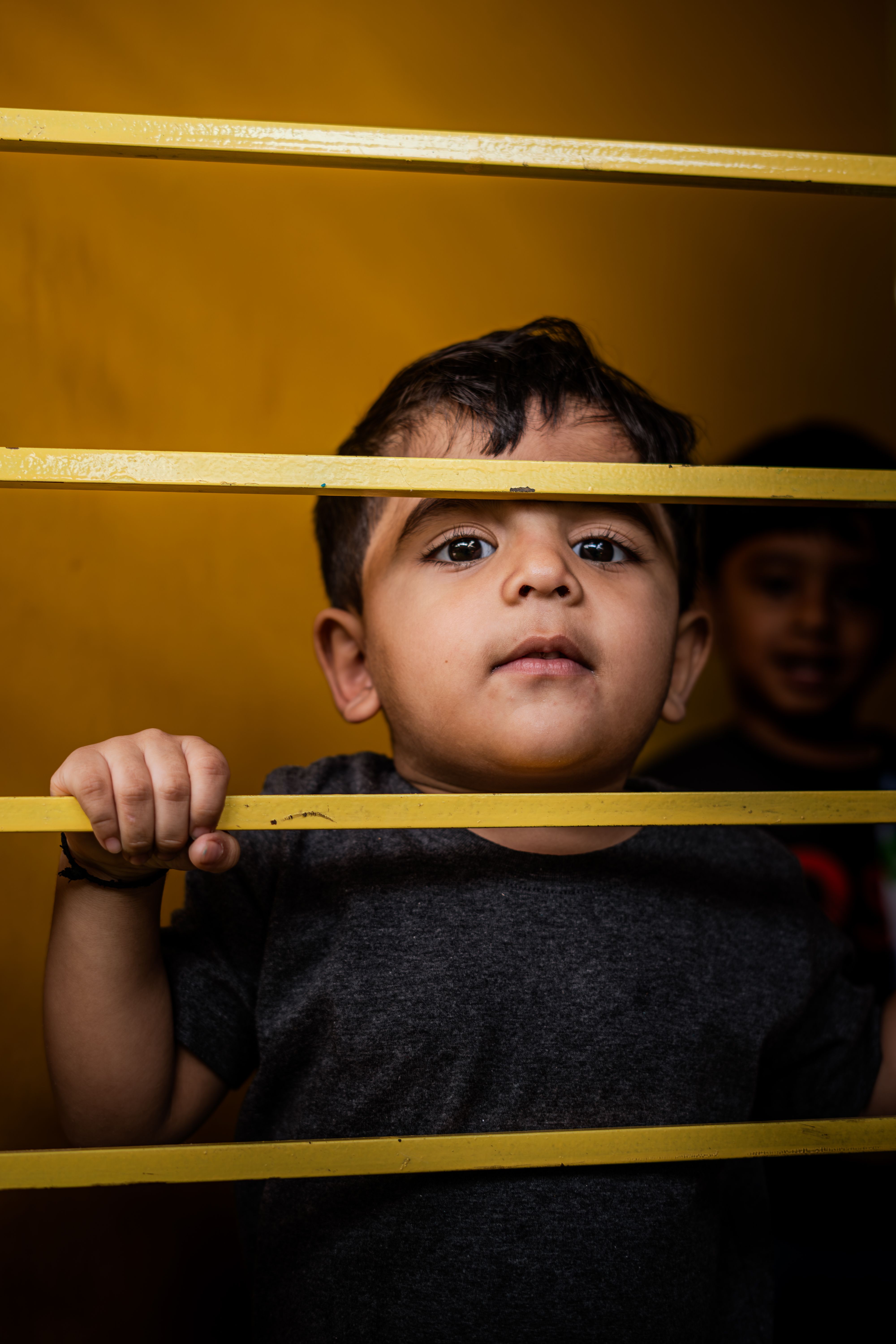 Curious Child Looking Through Yellow Bars Indoors · Free Stock Photo