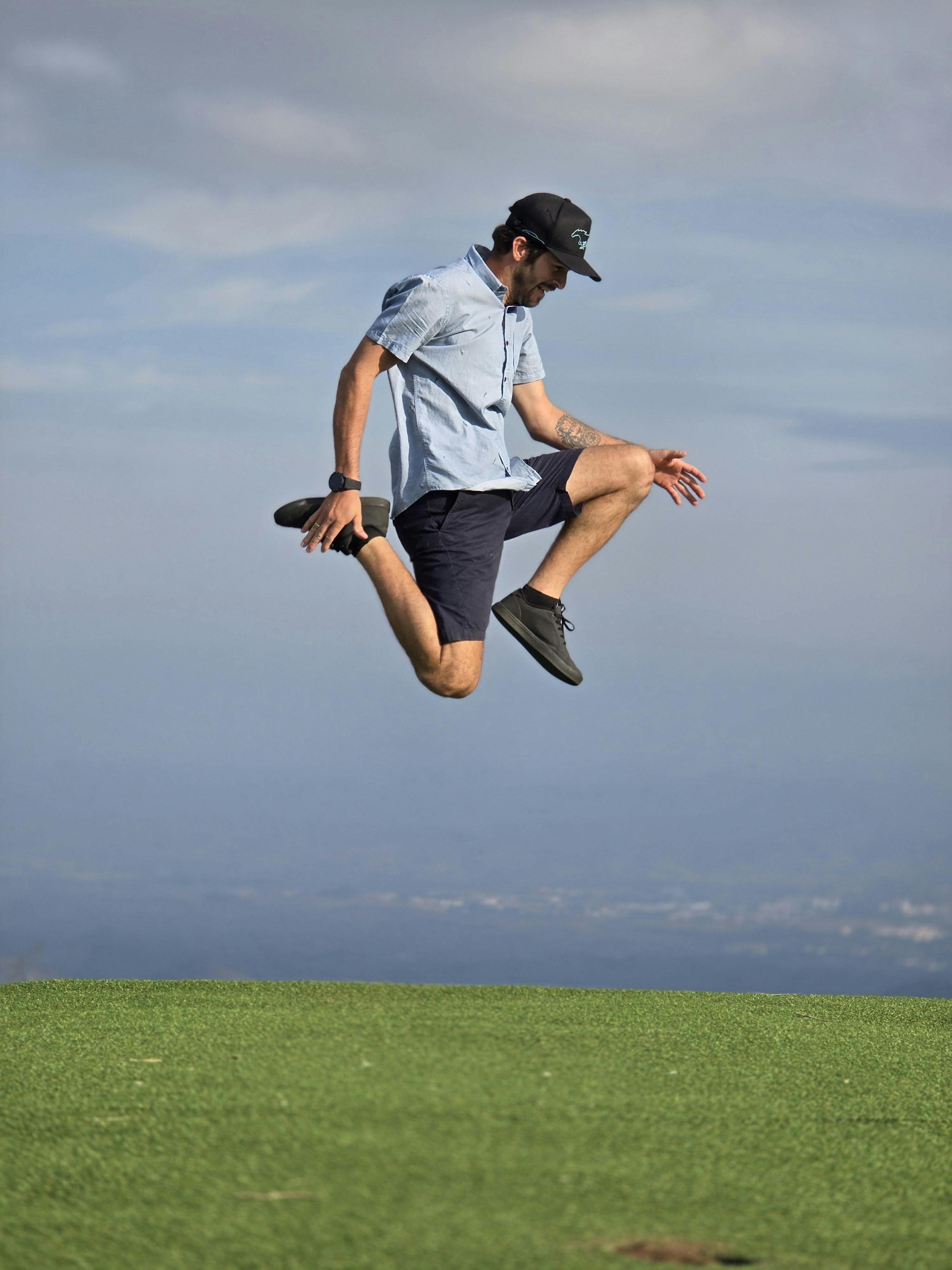Man Jumping Mid-air on a Grassy Hilltop · Free Stock Photo
