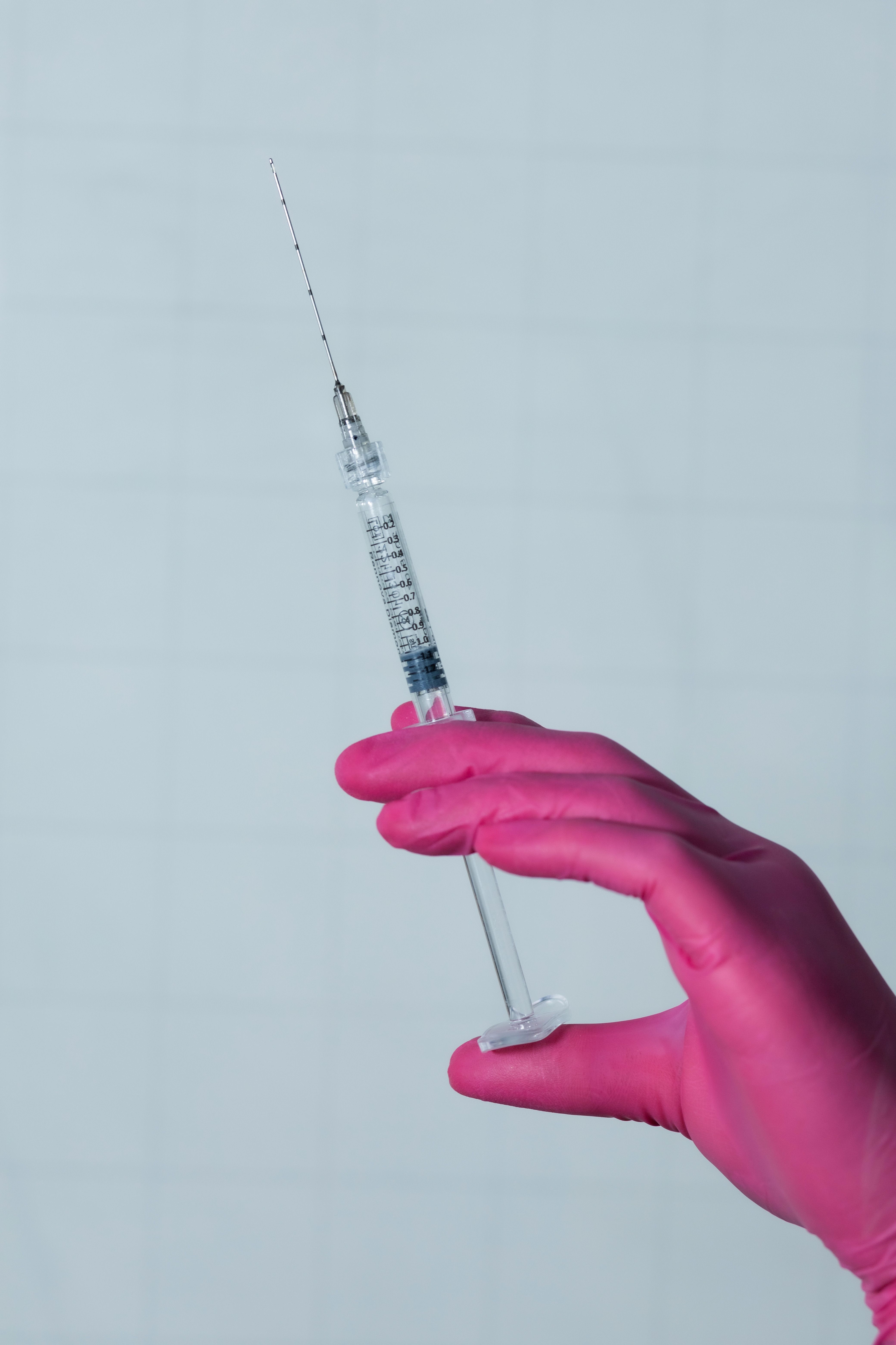 Gloved Hand Holding a Syringe Against Light Background · Free Stock Photo
