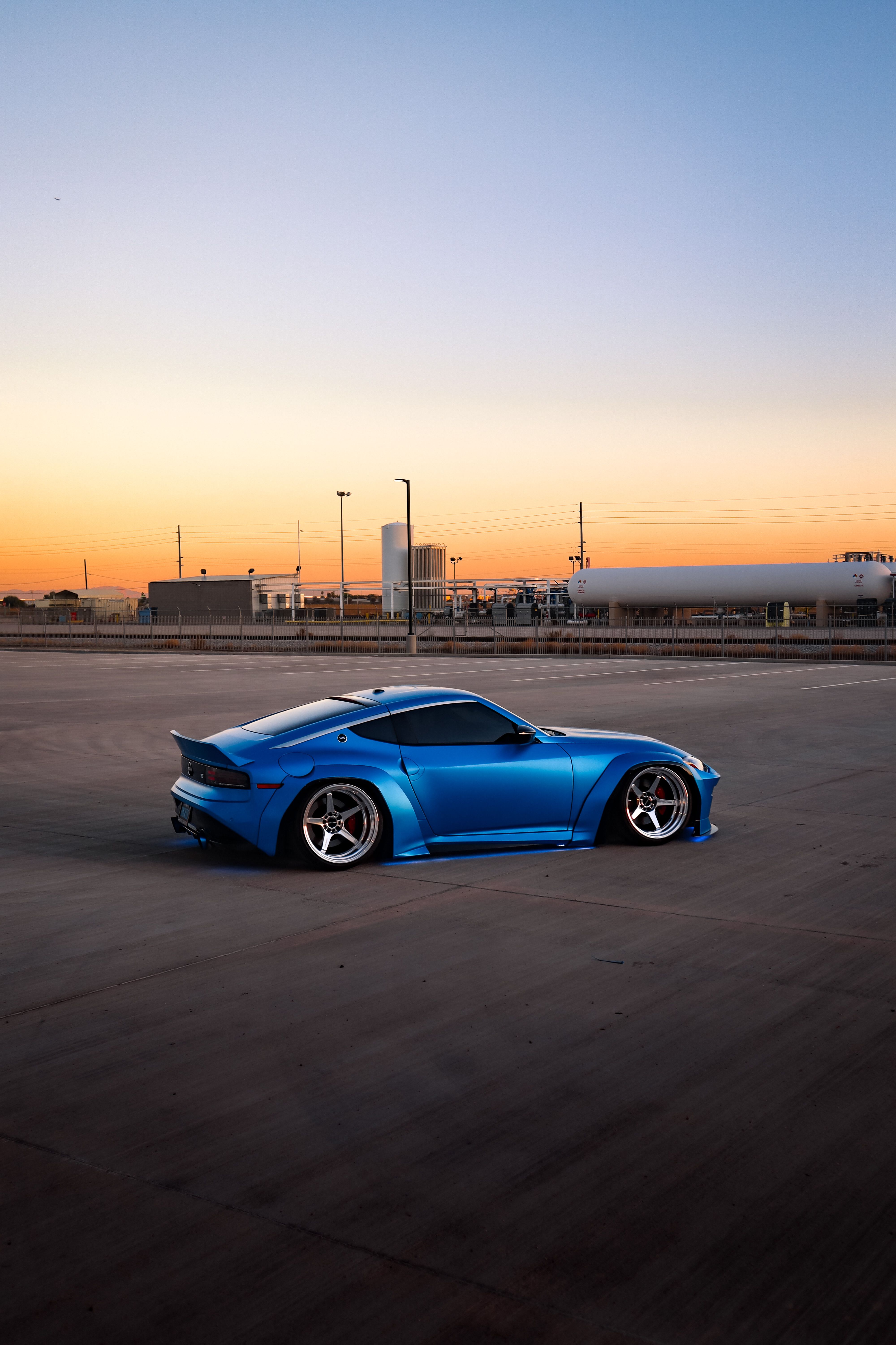 Blue sports car at sunset in industrial setting · Free Stock Photo