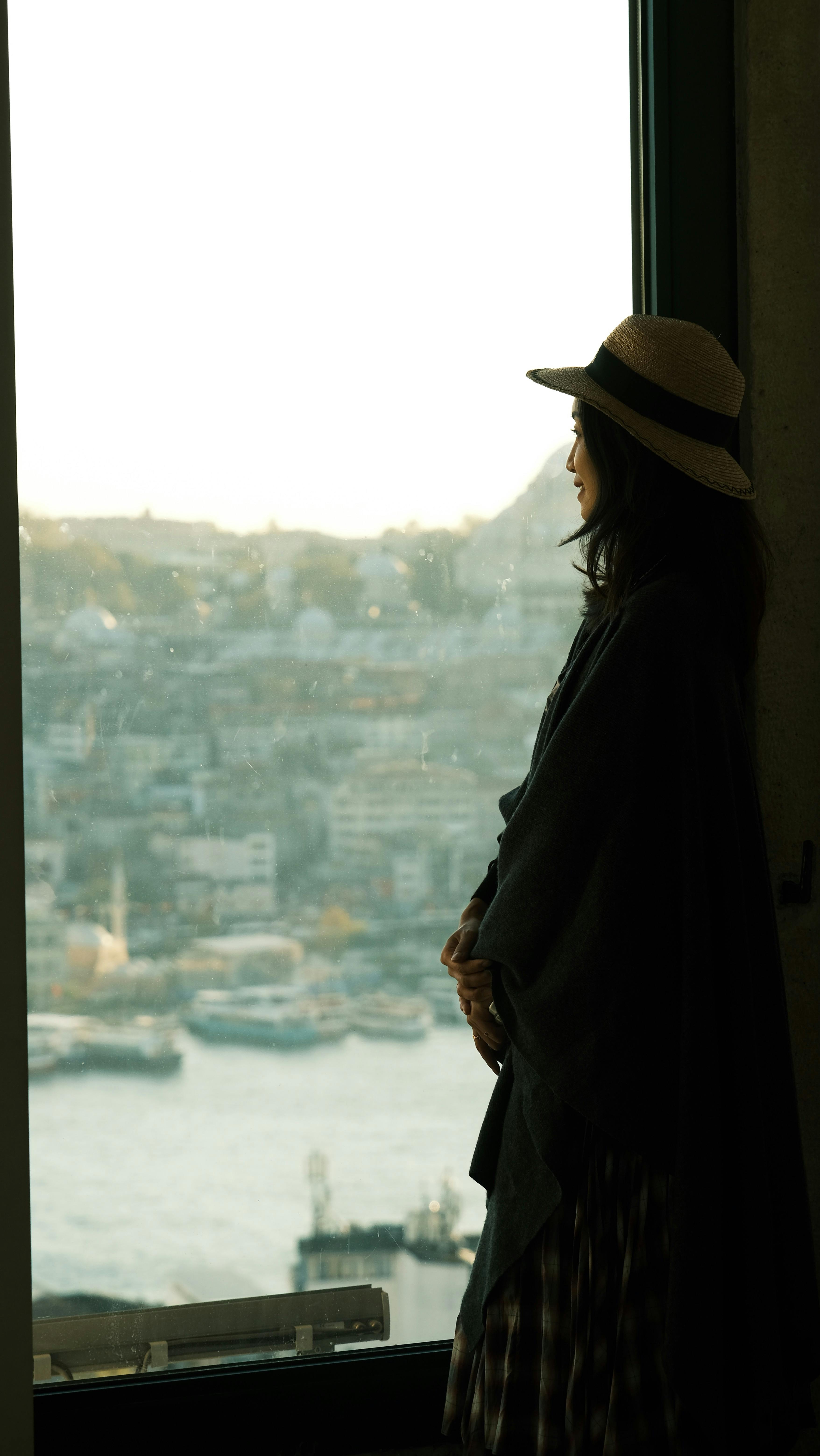 Woman Gazing Through Window Overlooking Cityscape · Free Stock Photo