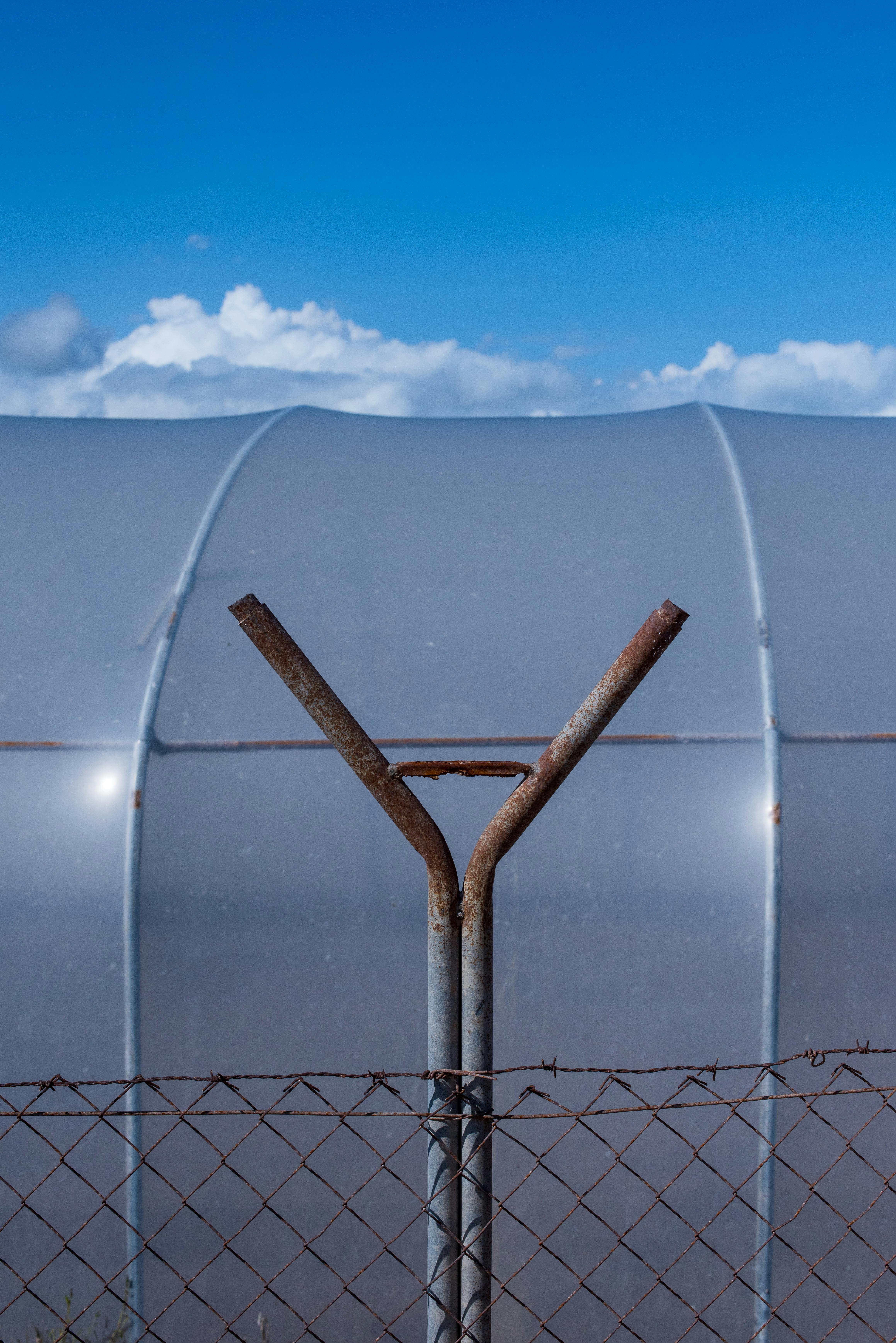 Rusty Fence Post and Industrial Greenhouse · Free Stock Photo