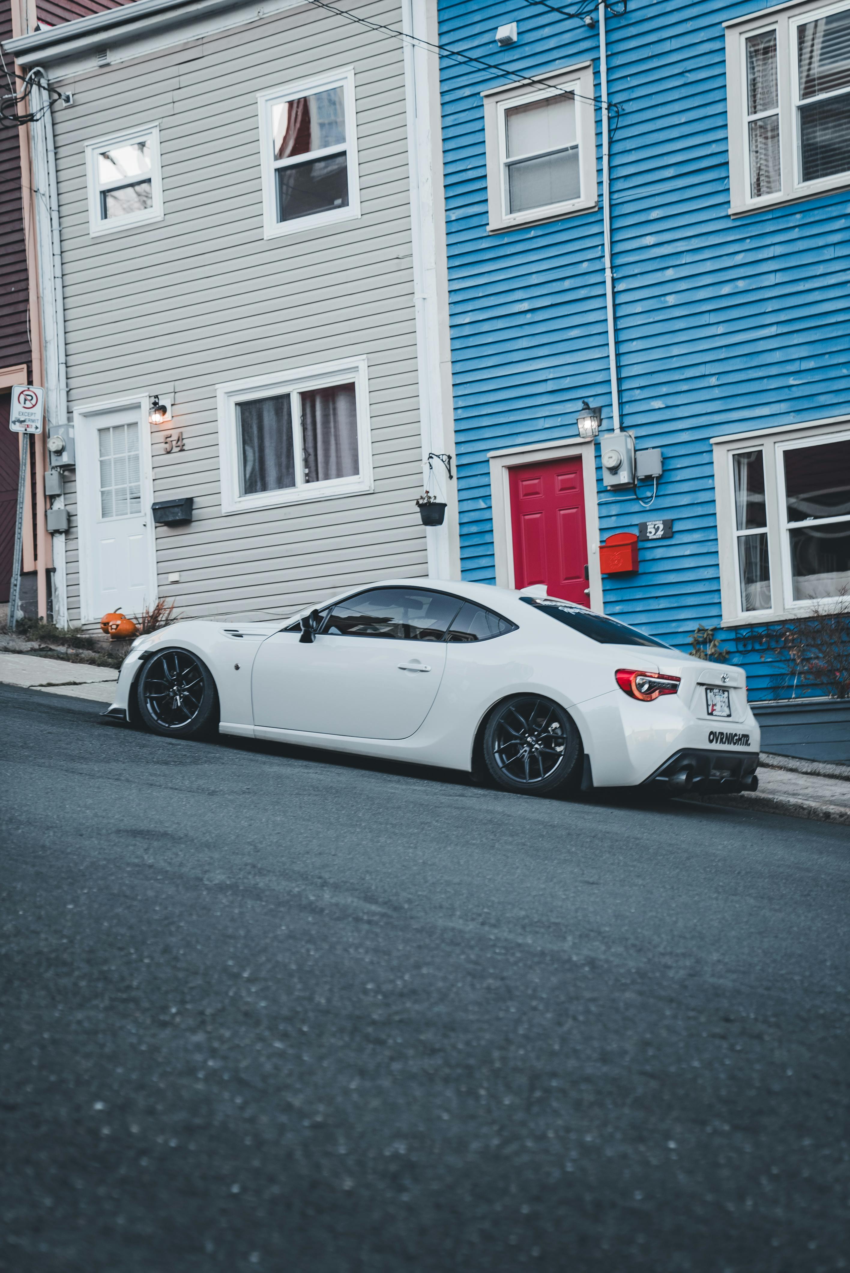 Sleek White Car Parked on Urban Street, Vibrant Houses · Free Stock Photo