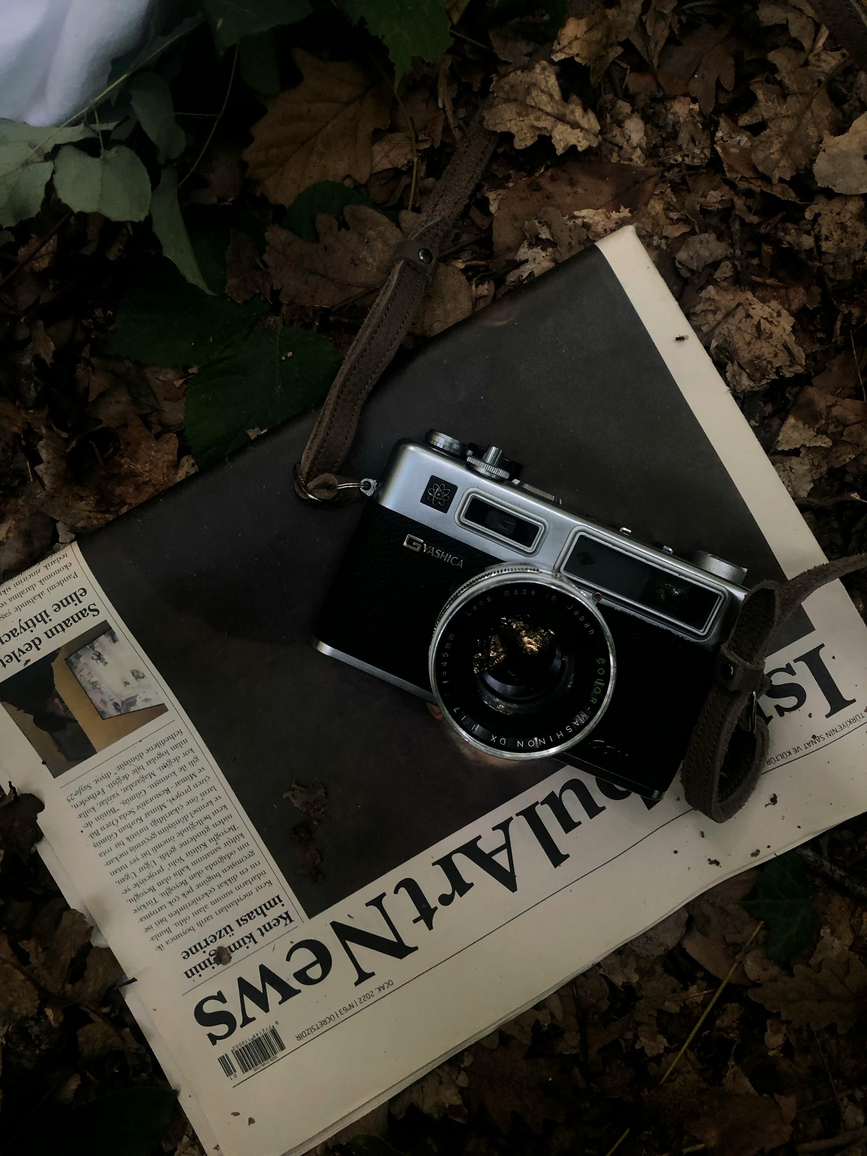 Vintage Camera Resting on Newspaper Outdoors · Free Stock Photo