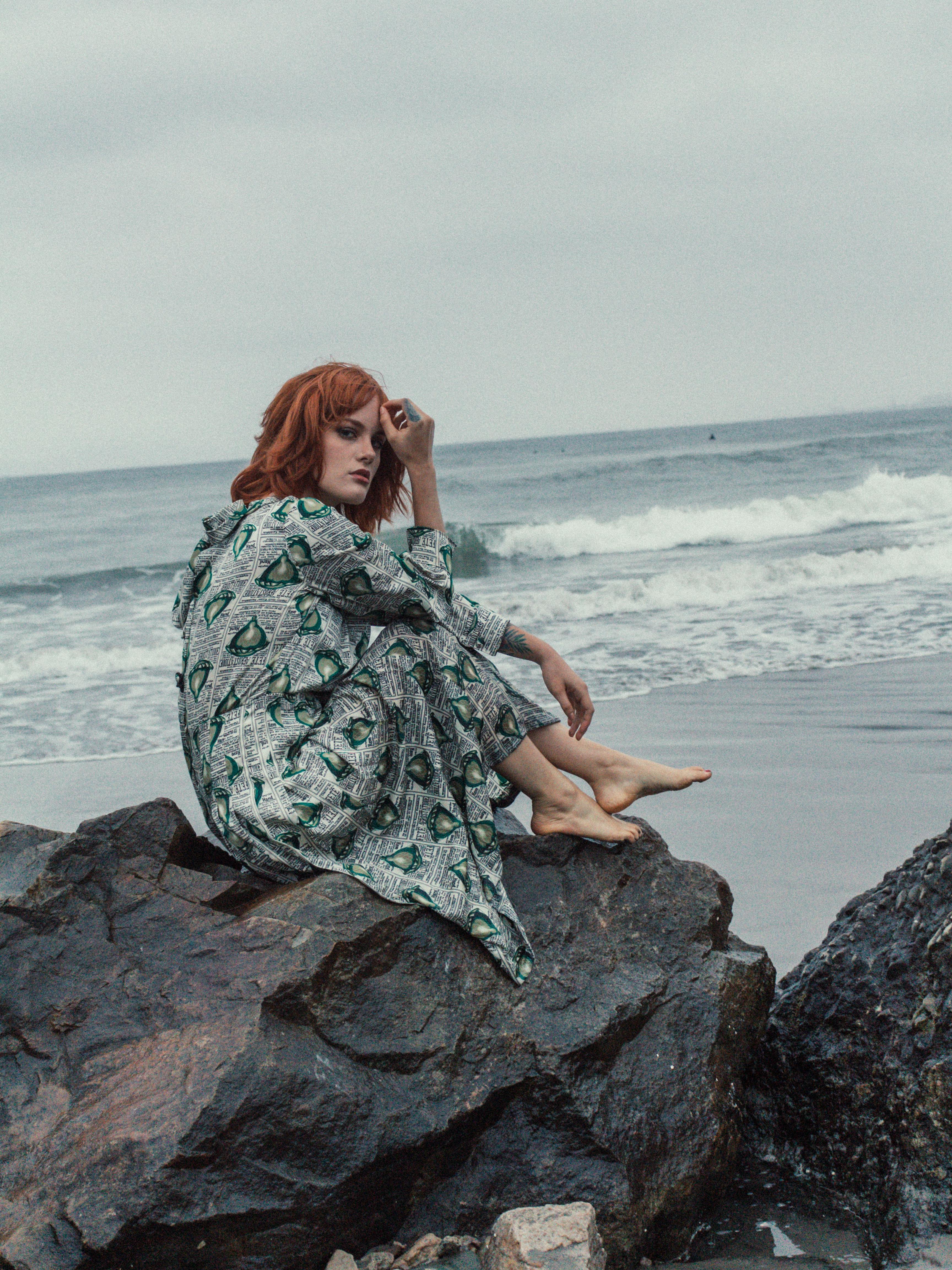 Woman in Patterned Robe on Coastal Rocks · Free Stock Photo