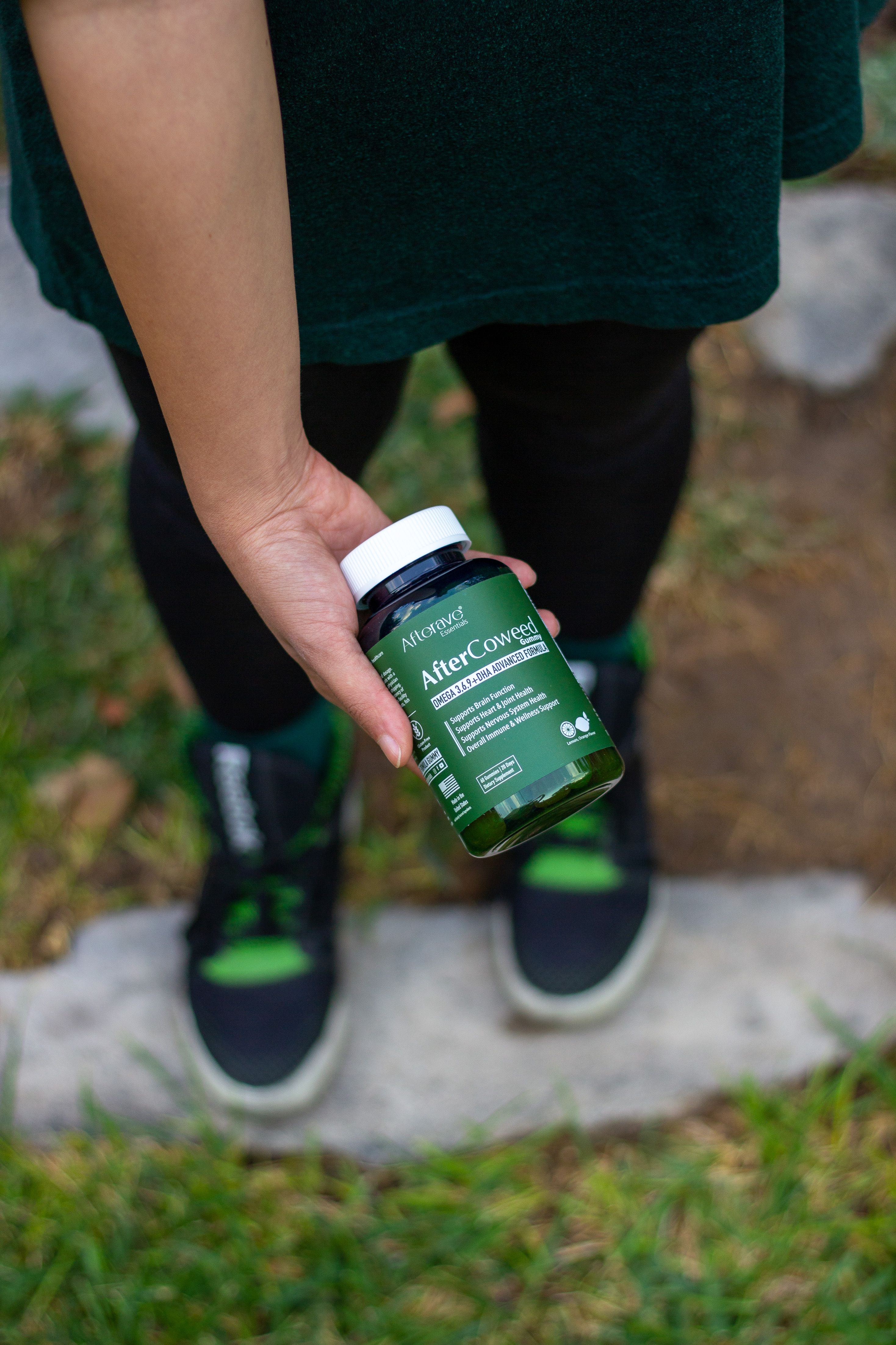 Person Holding Green Supplement Bottle Outdoors · Free Stock Photo