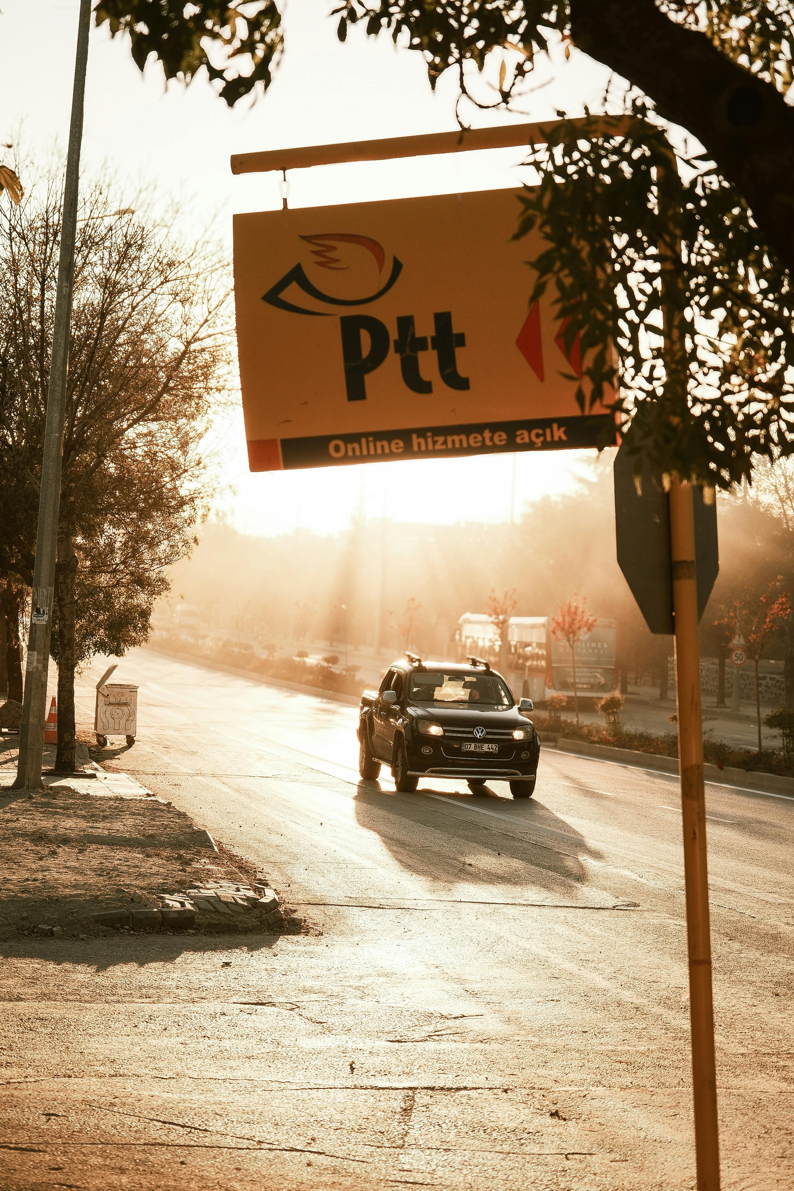 Sunlit Street with PTT Sign and Car Driving · Free Stock Photo