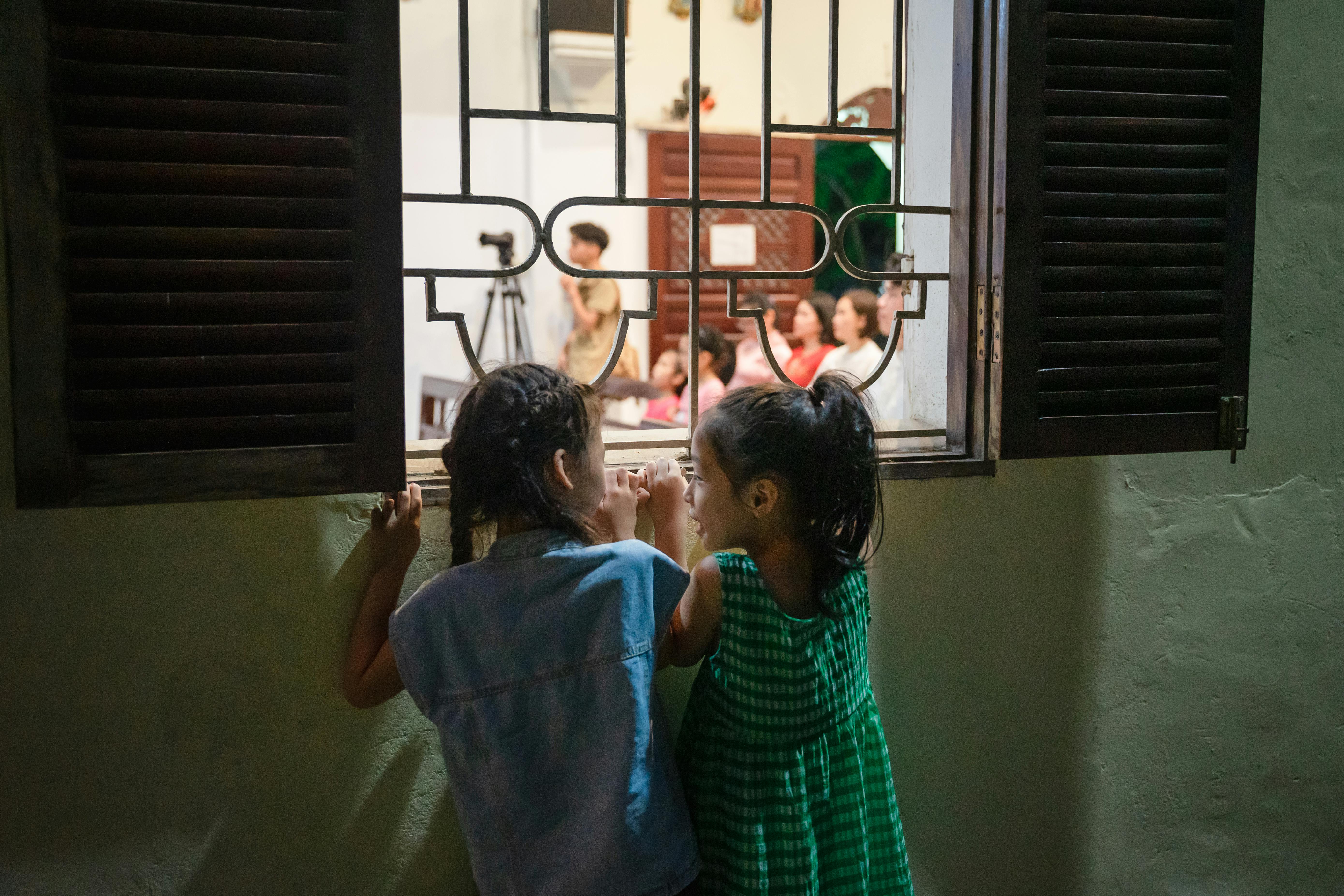 Two Children Peering into a Room through Window Bars · Free Stock Photo