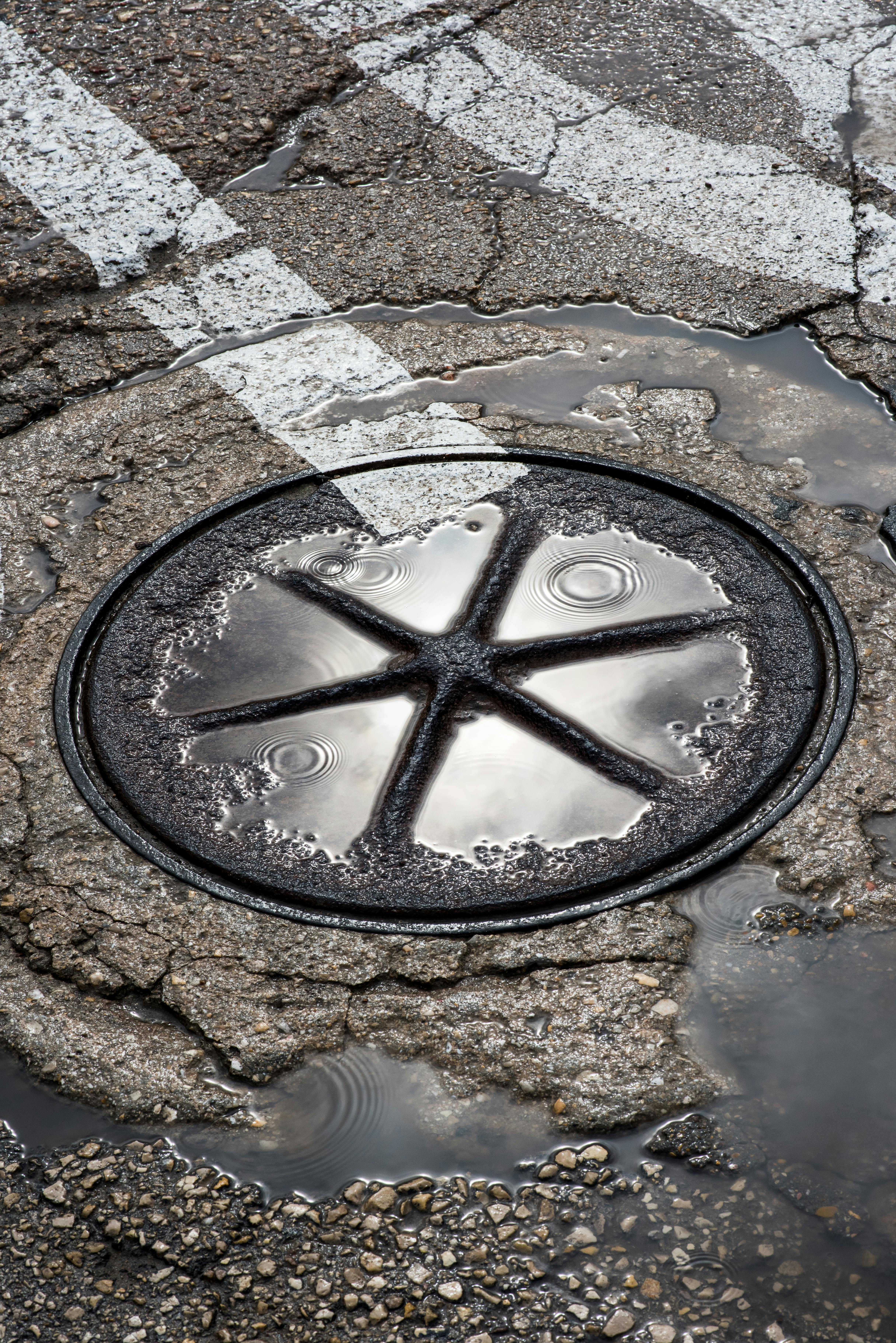 Wet Manhole Cover with Reflective Puddles · Free Stock Photo