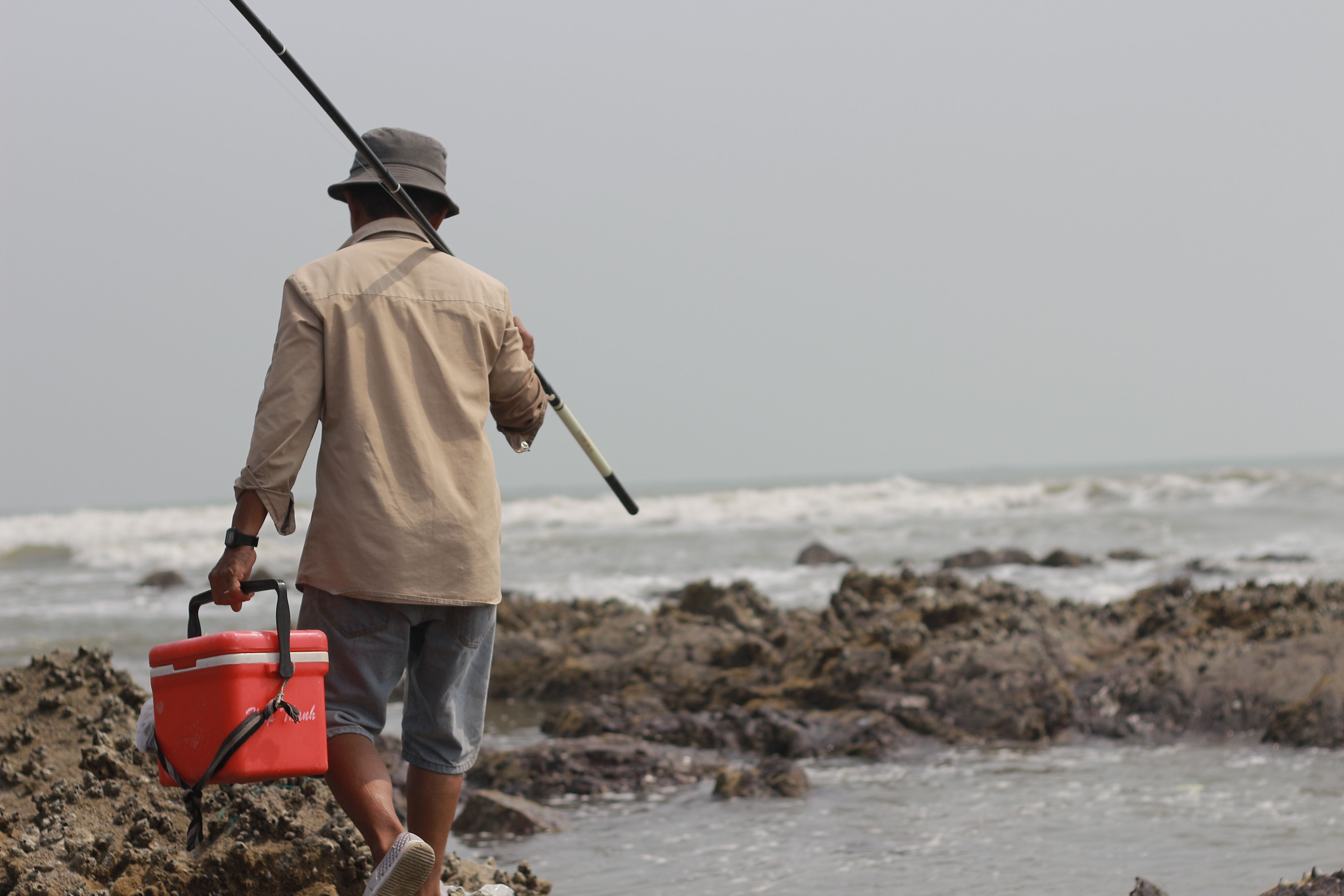Fisherman Walking on Rocky Shoreline with Gear · Free Stock Photo