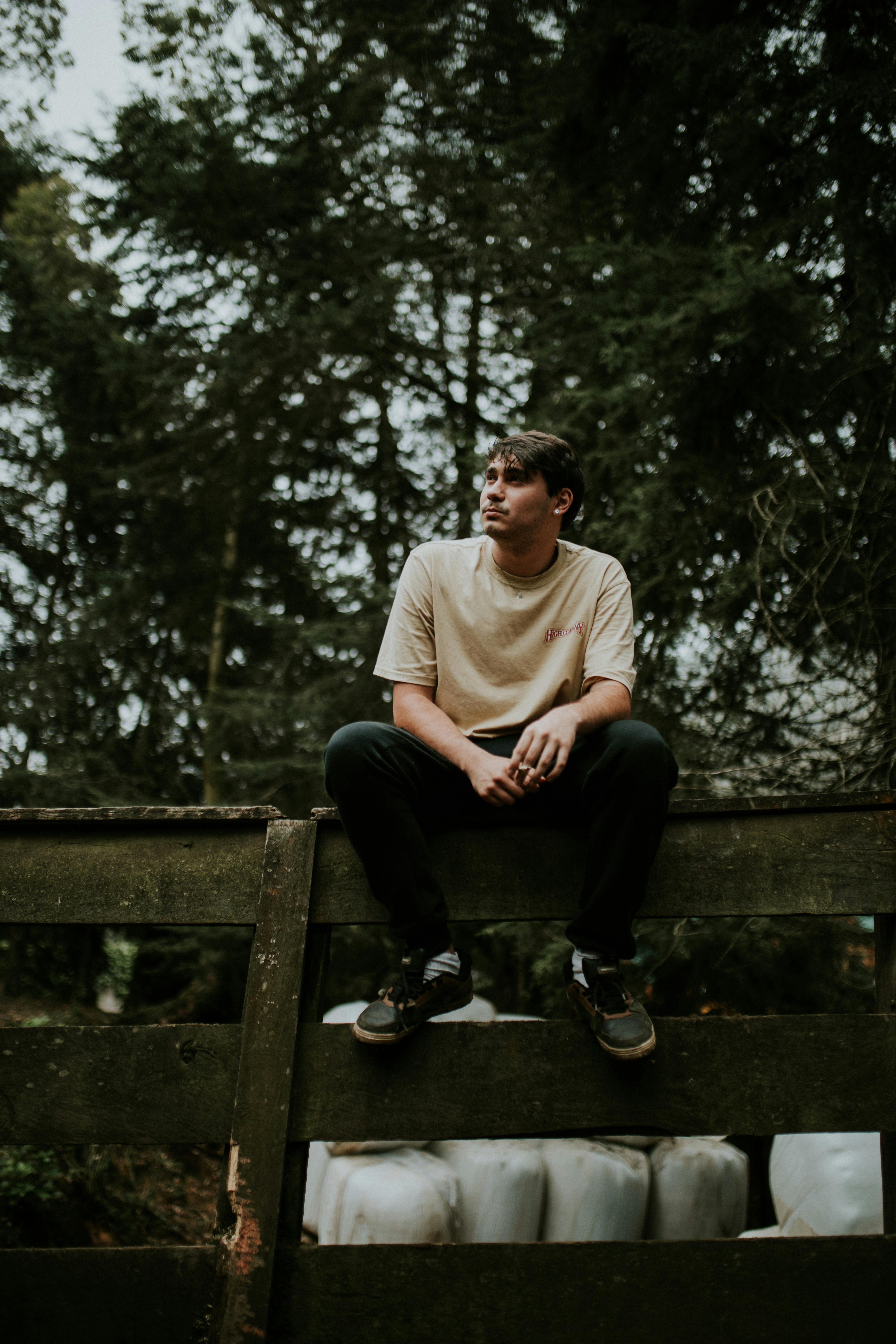 Young Man Sitting on Fence in Forested Area · Free Stock Photo