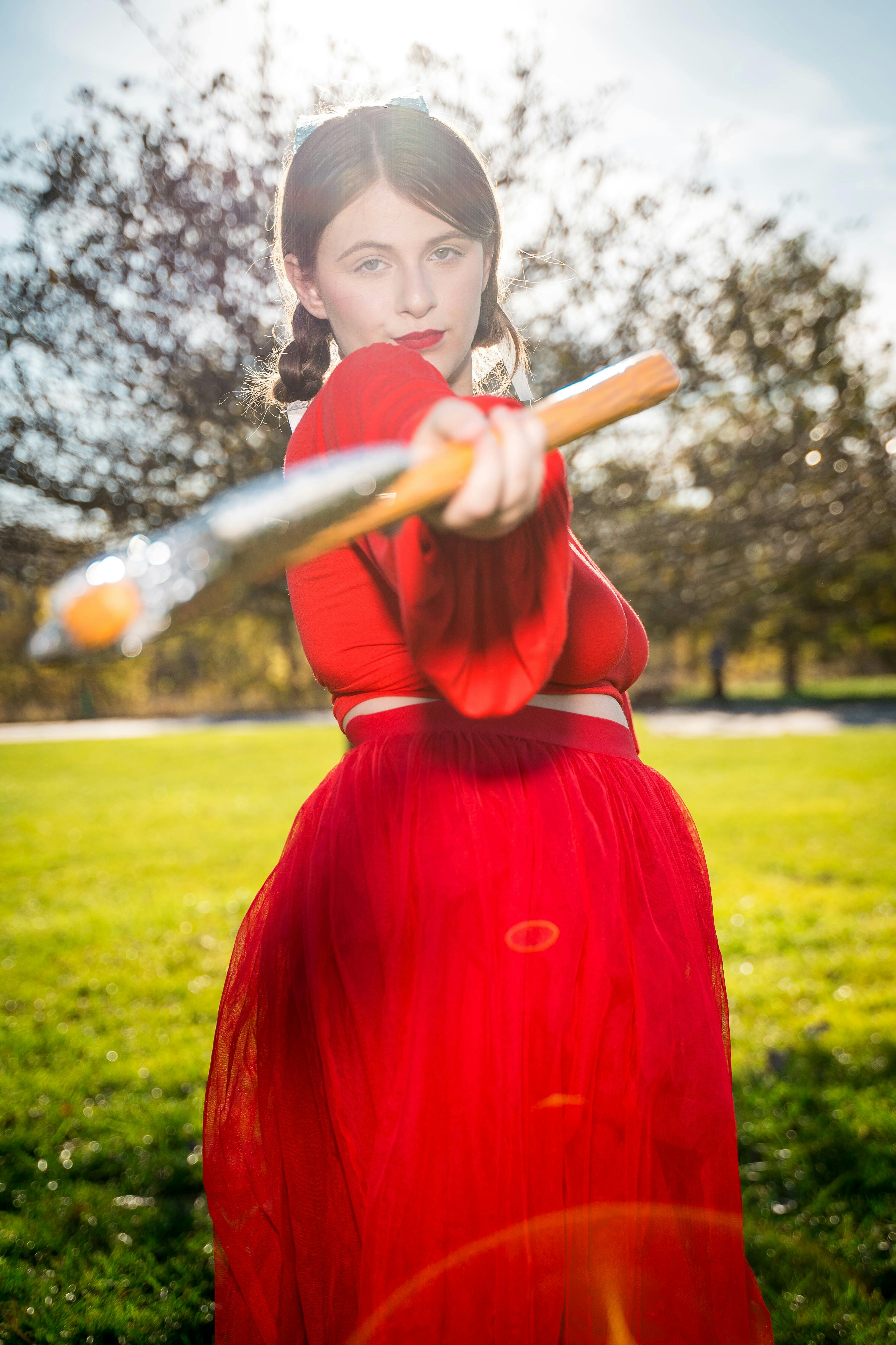 Young Woman Wielding Bat Outdoors in Red Costume · Free Stock Photo