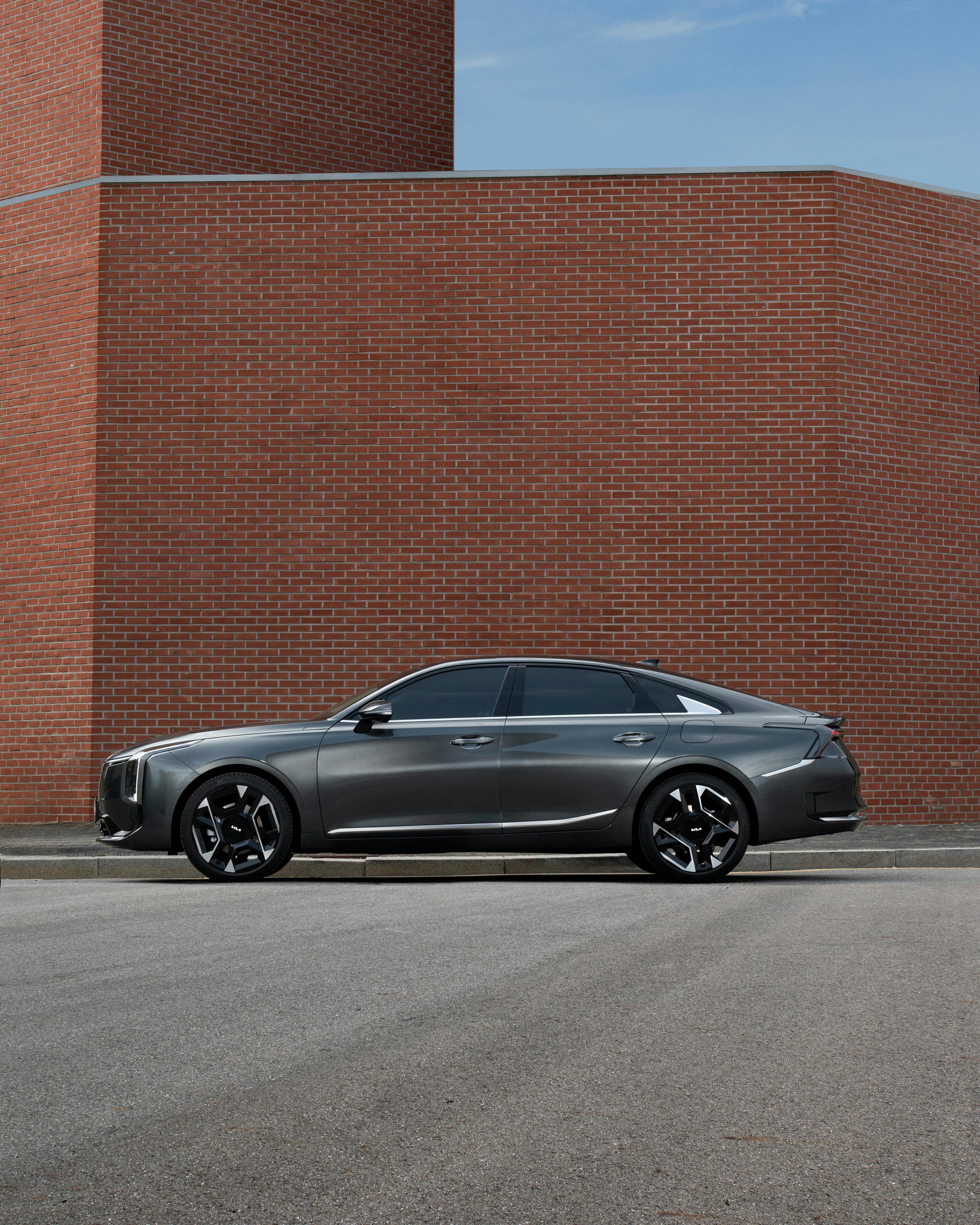 Sleek Grey Sedan Against a Brick Wall Outdoors · Free Stock Photo