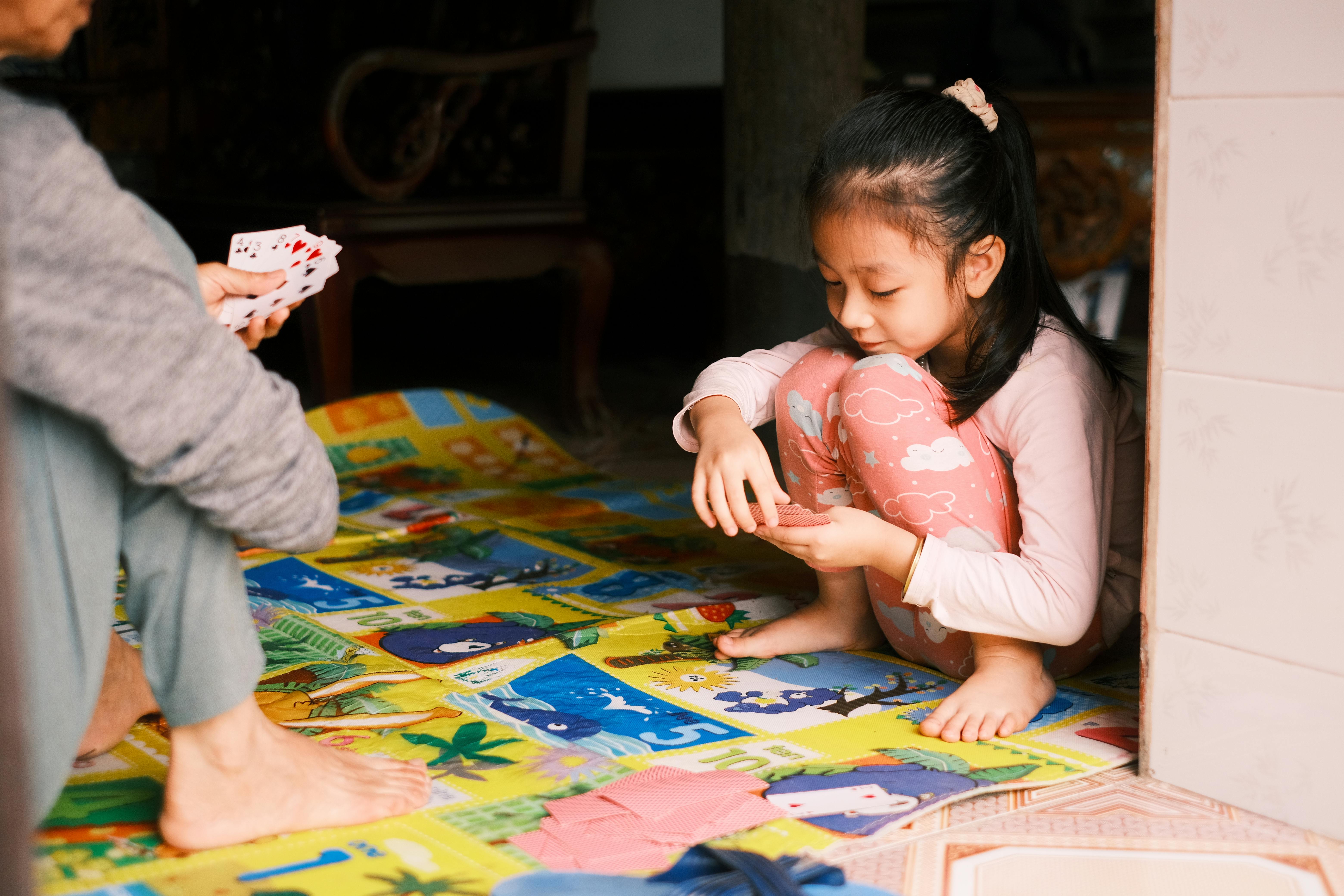 Child Playing Cards Indoors on Colorful Mat · Free Stock Photo
