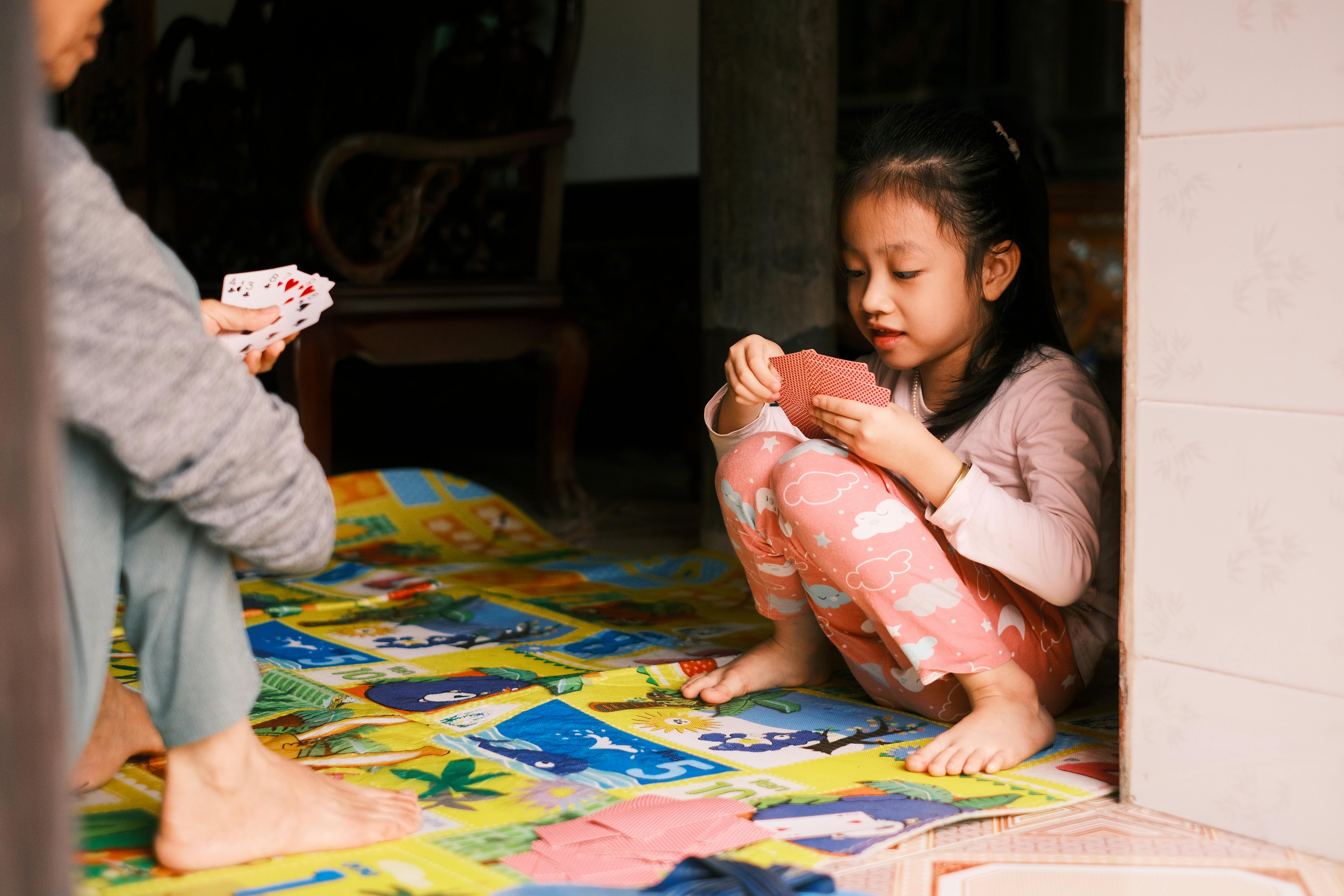 Child Playing Cards Indoors with Family · Free Stock Photo