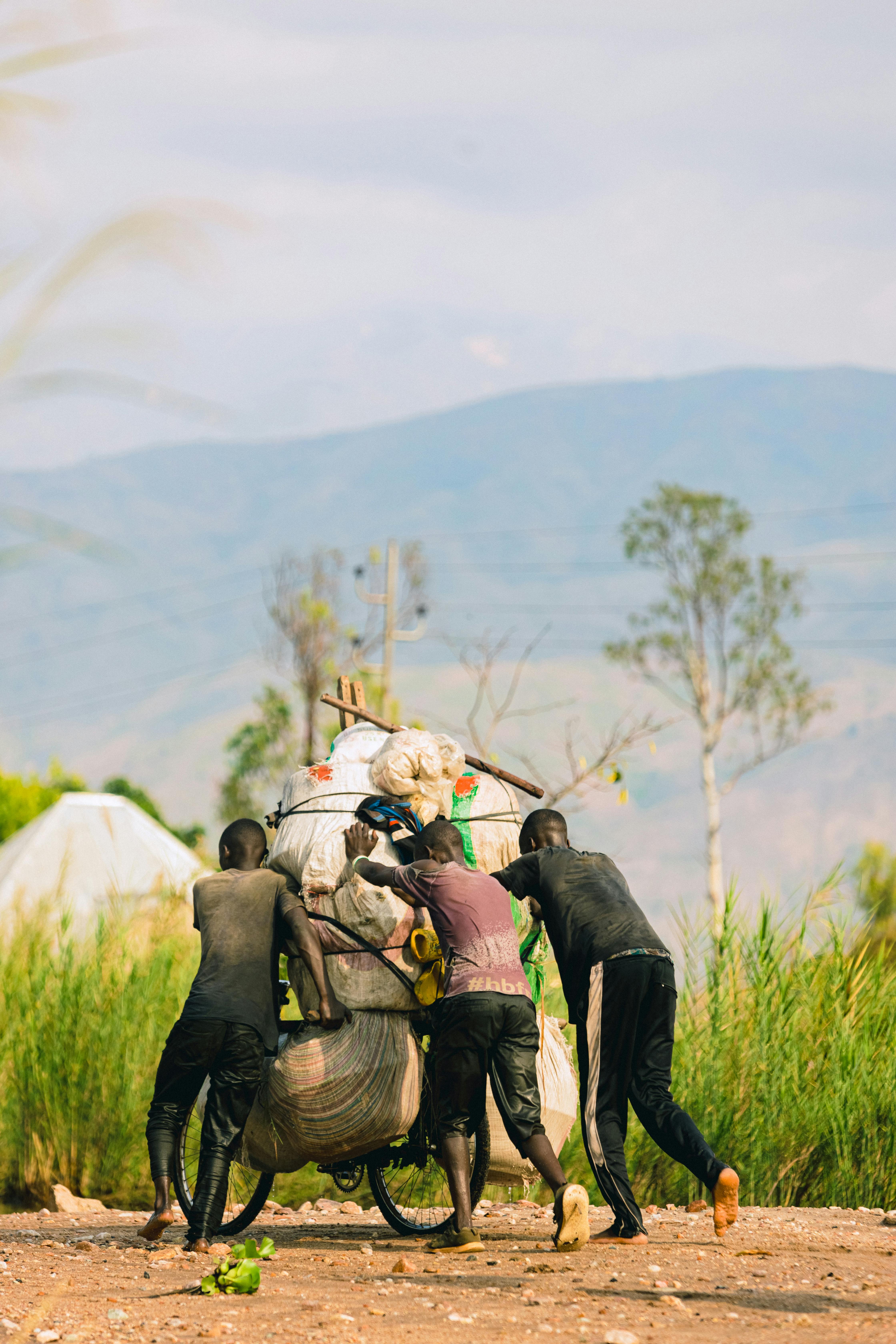 Three Men Pushing a Loaded Bicycle Outdoors · Free Stock Photo