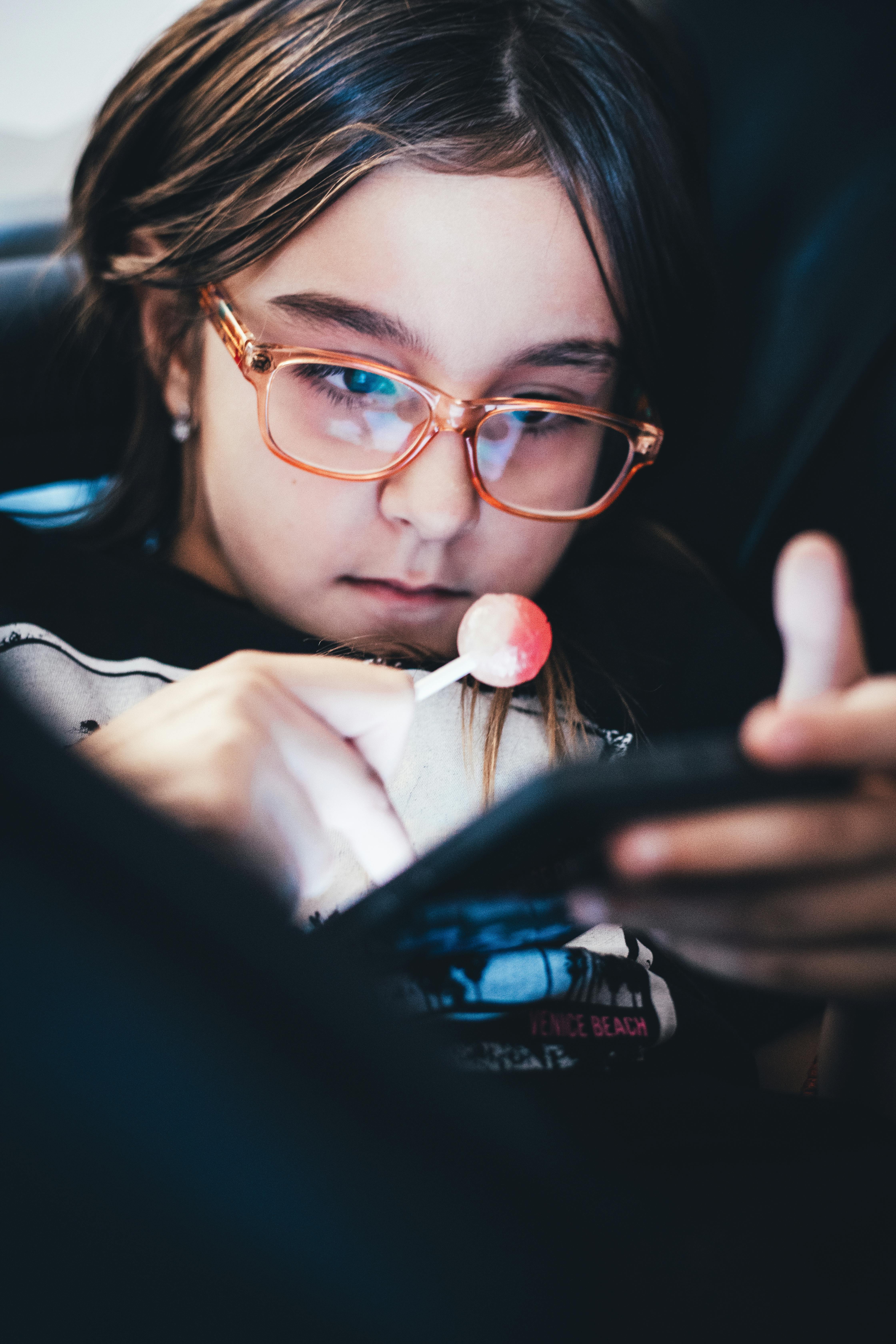 Child using smartphone while eating candy indoors · Free Stock Photo