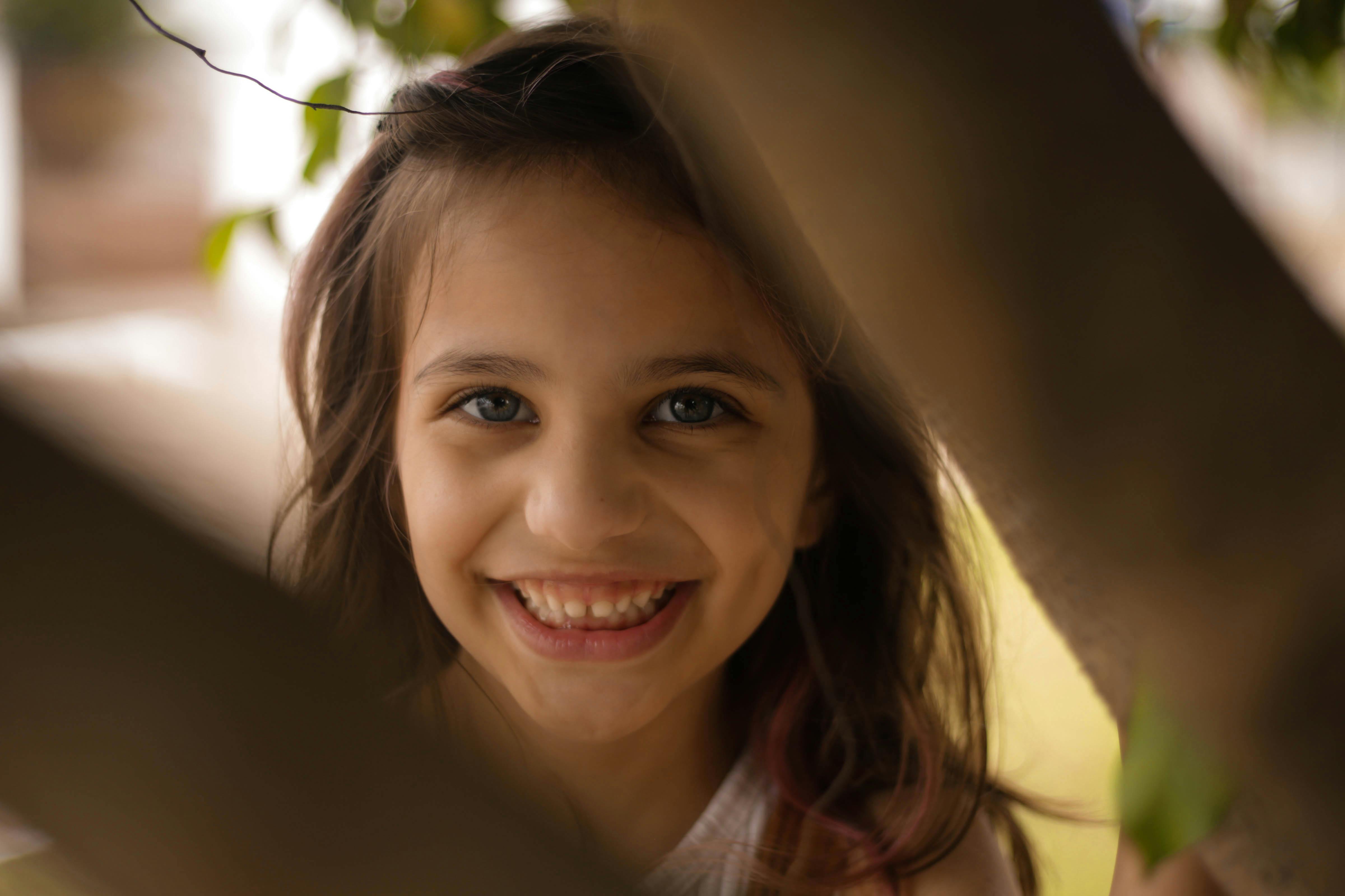 Smiling Child Peeking Through Tree Branches · Free Stock Photo