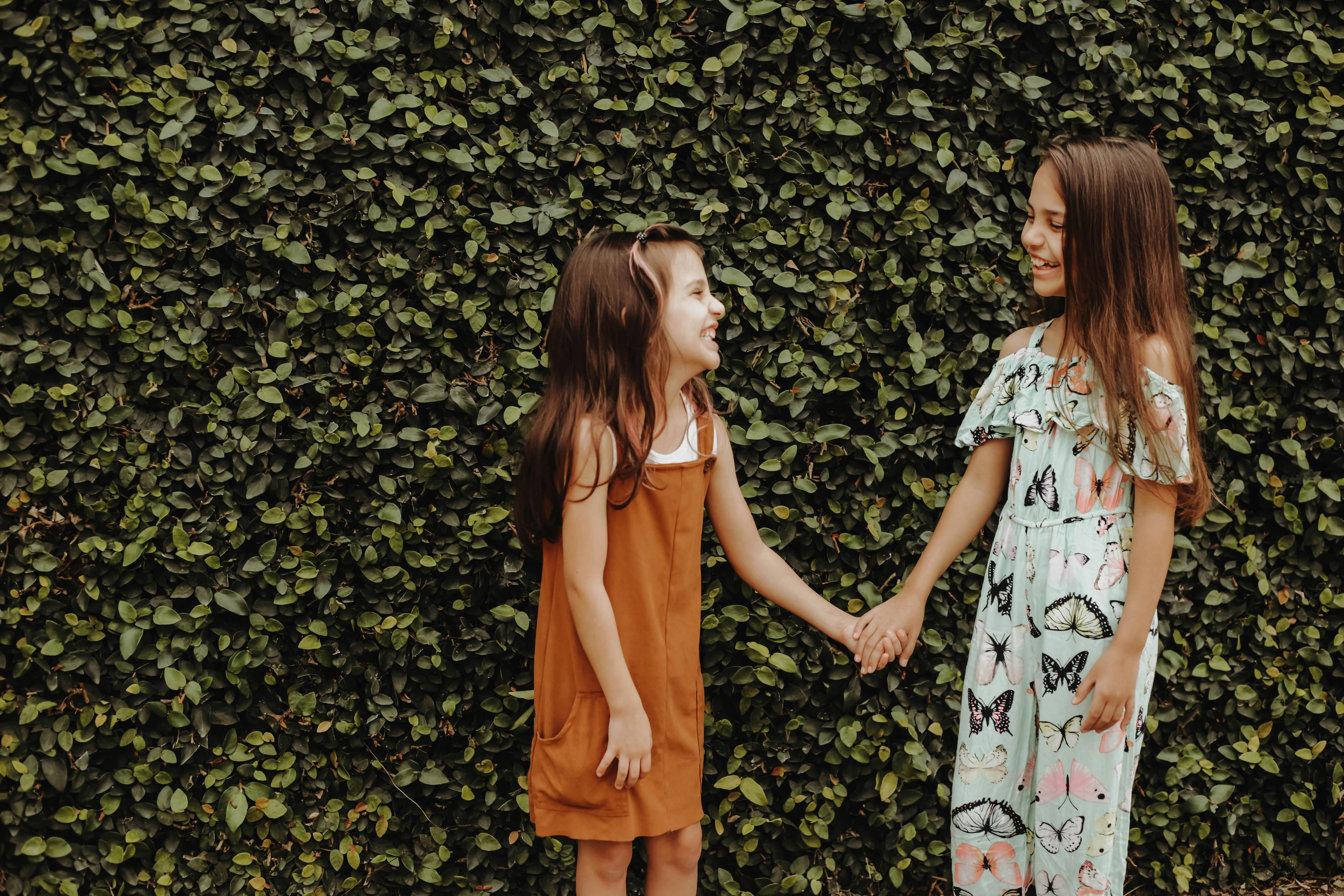 Two girls holding hands in front of lush foliage · Free Stock Photo