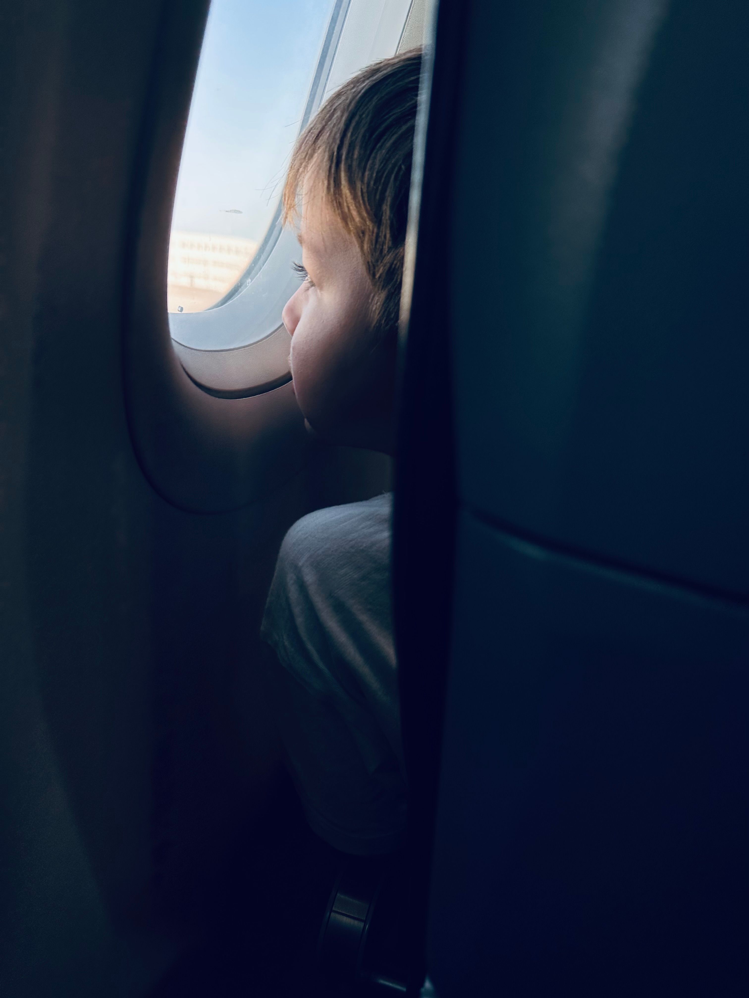 Child gazing through airplane window during flight · Free Stock Photo