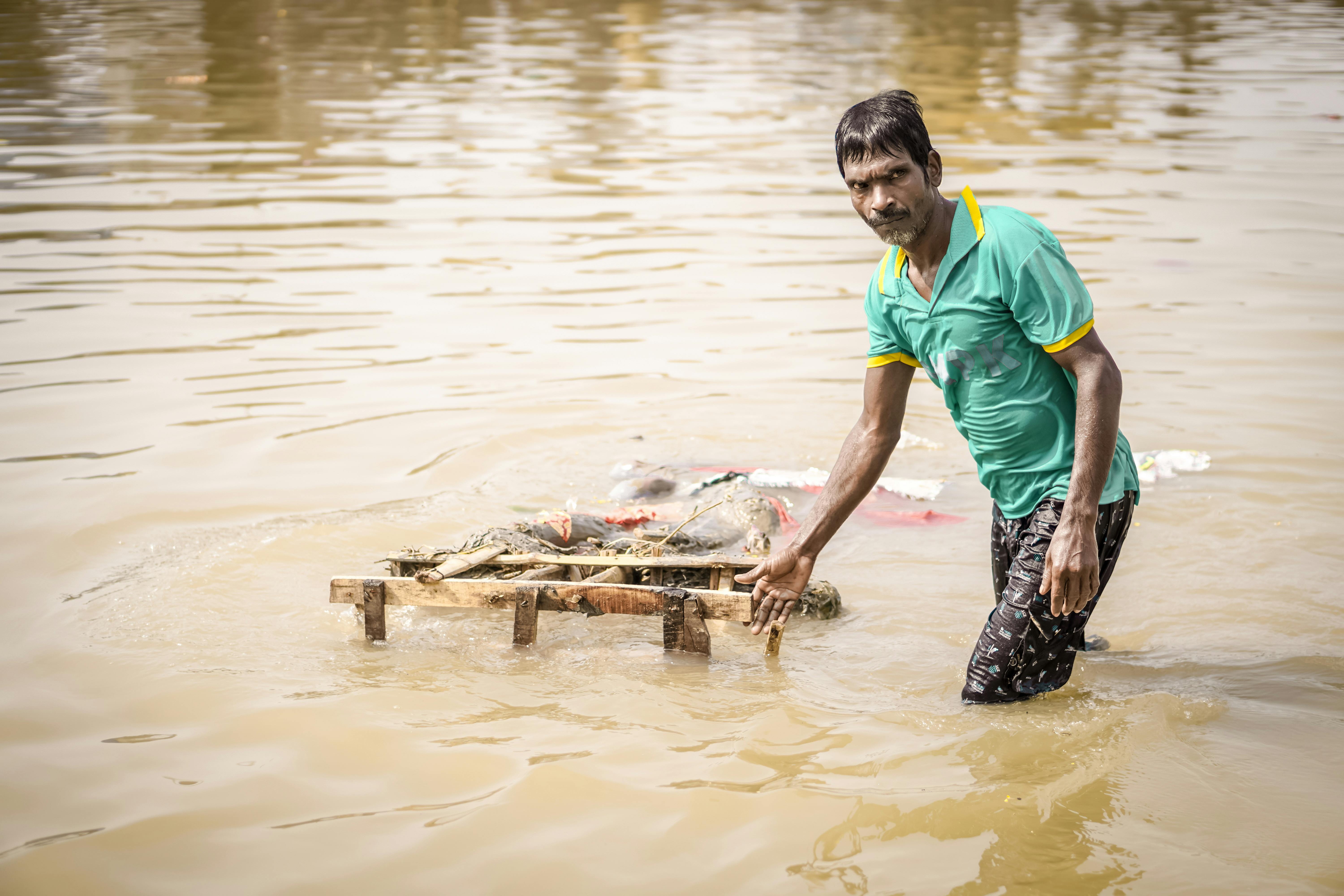 Man in Water Pulling a Wooden Raft in Bright Daylight · Free Stock Photo