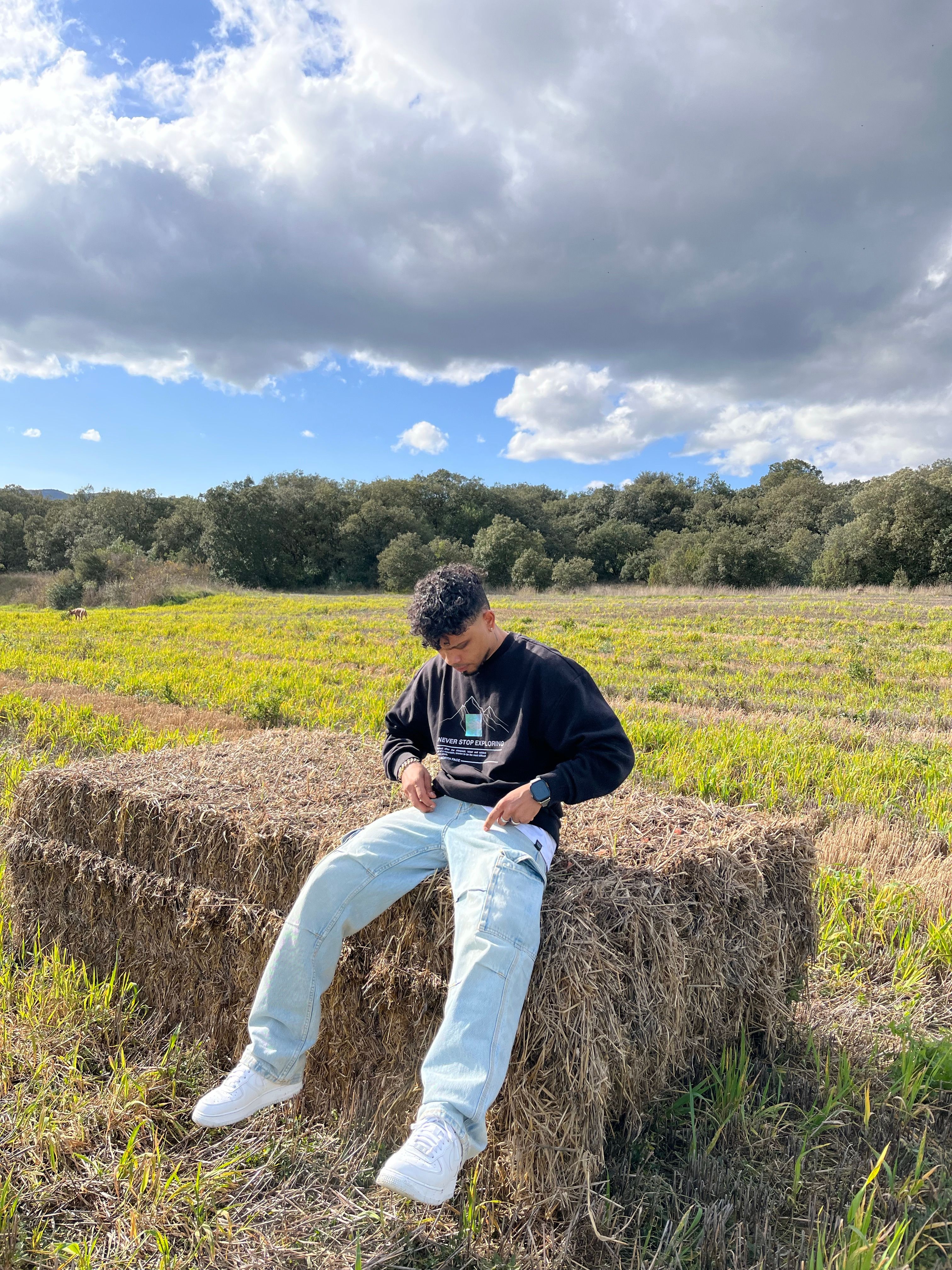 Young man sitting on hay bale in rural field · Free Stock Photo