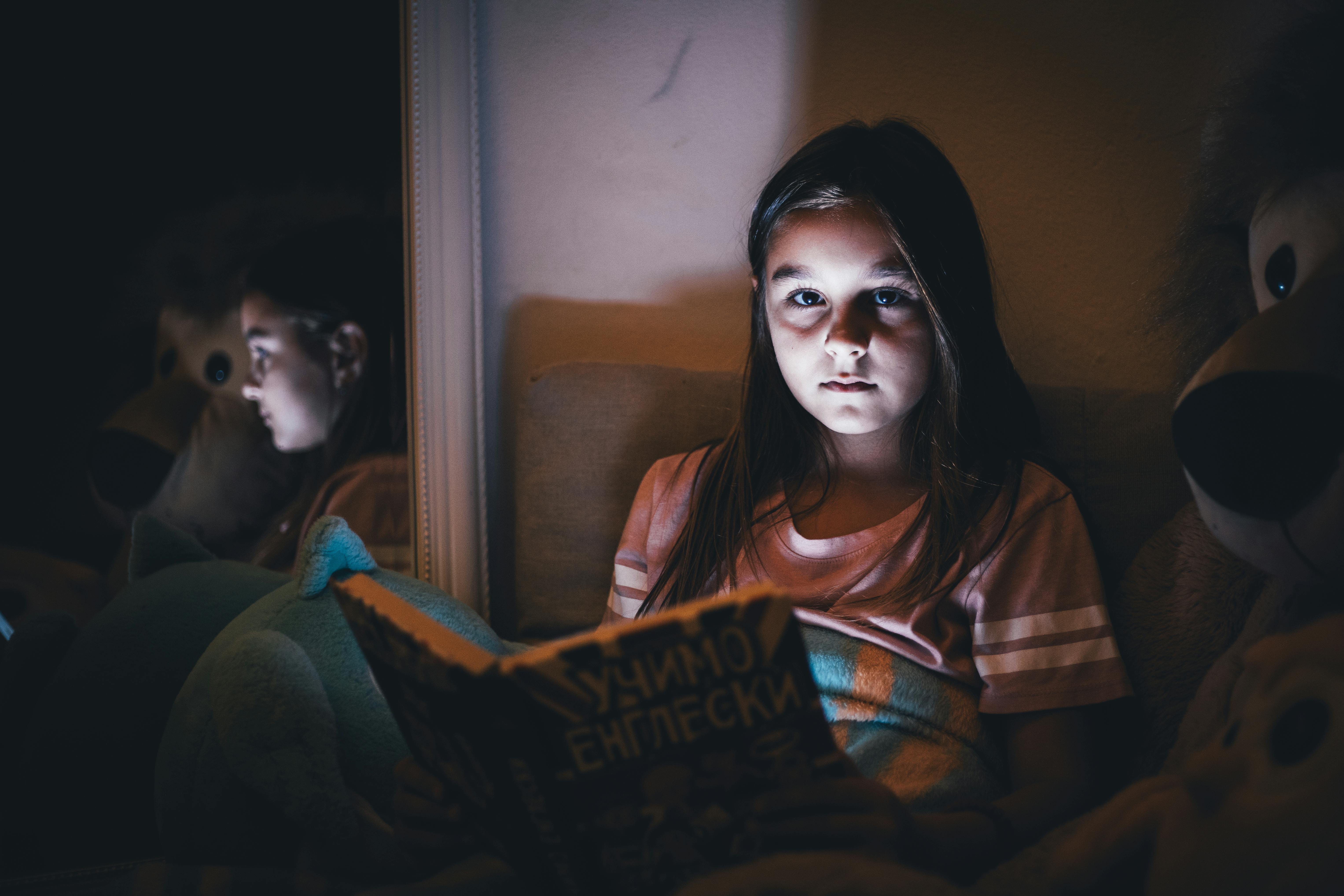 Child reading book at night in dimly lit room · Free Stock Photo