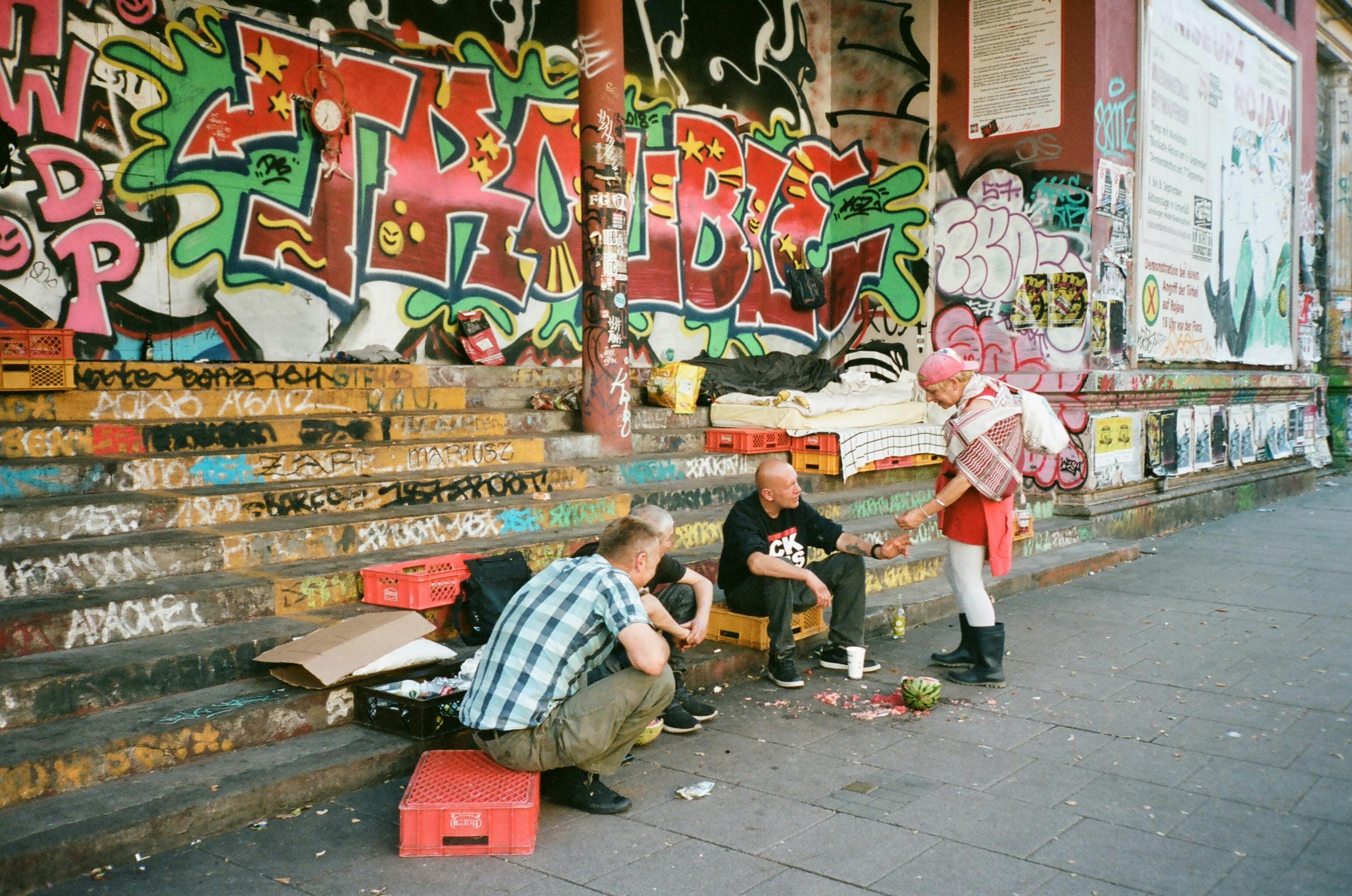 Man Standing in Front of Three Men Sitting on Stairs · Free Stock Photo