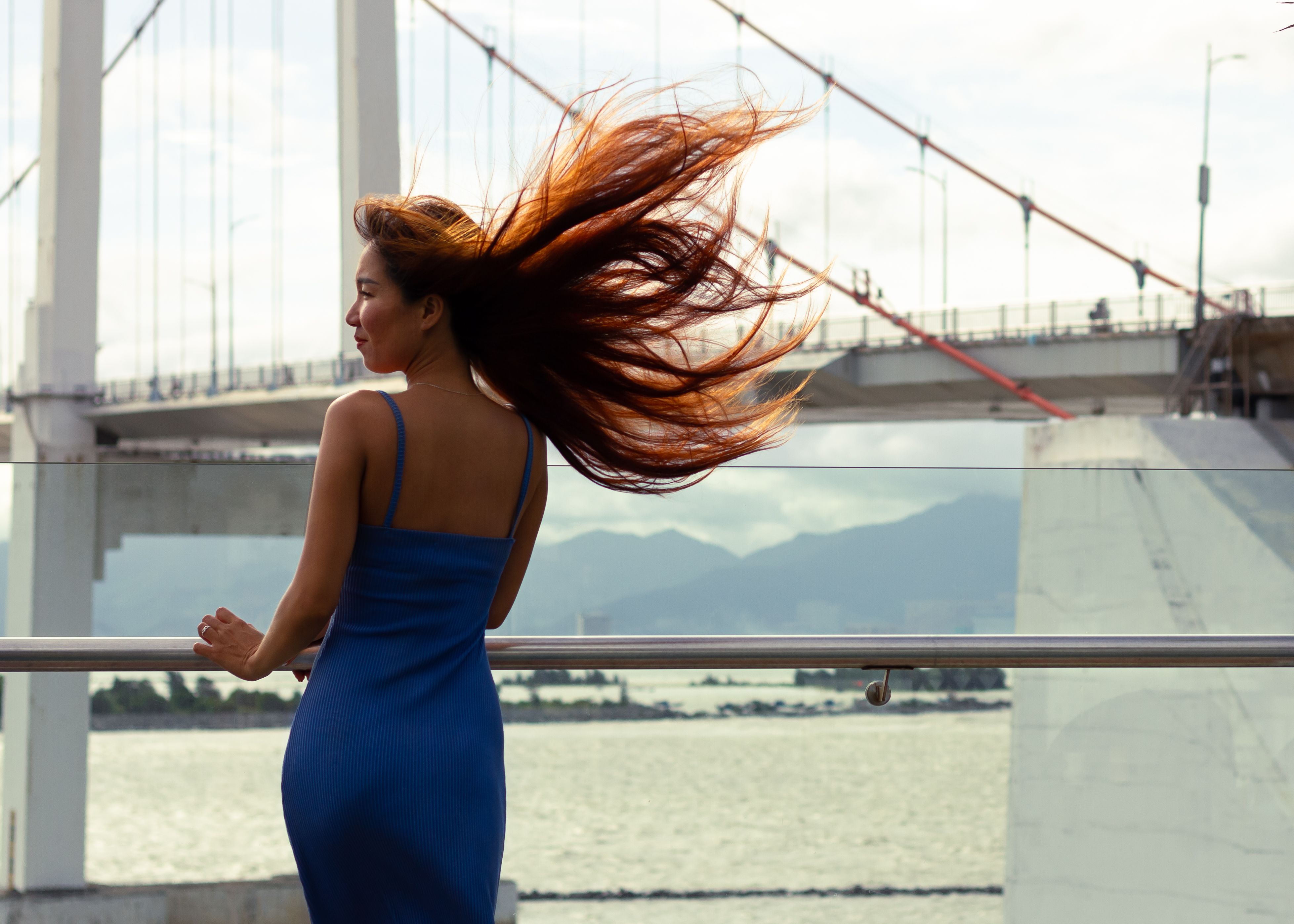 Woman in Blue Dress with Hair Blowing on Bridge · Free Stock Photo