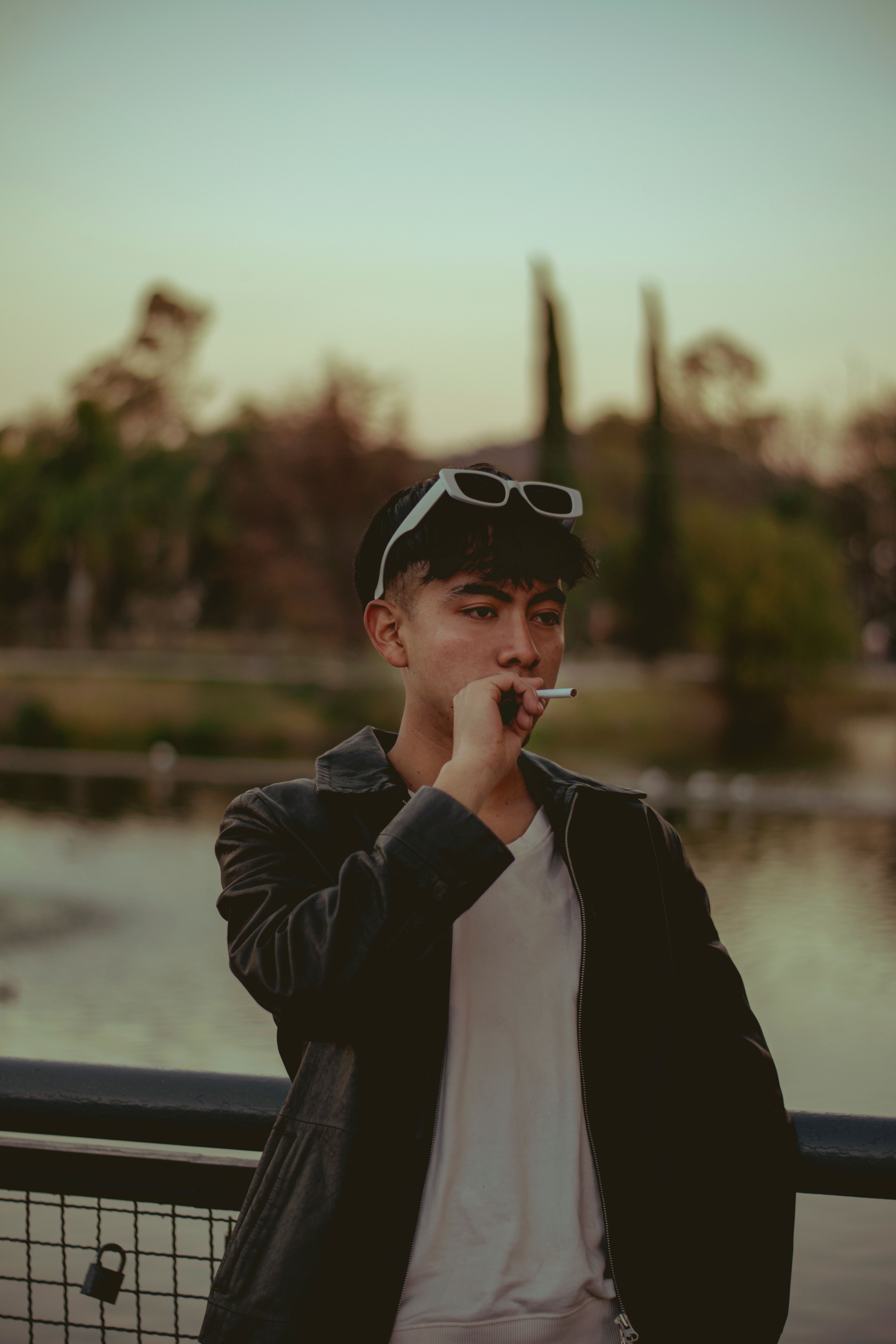 Contemplative Young Man Smoking by Lakeside Sunset · Free Stock Photo